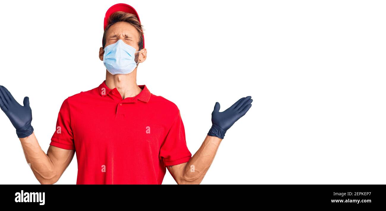 Handsome blond man with beard wearing delivery uniform and medical mask ...