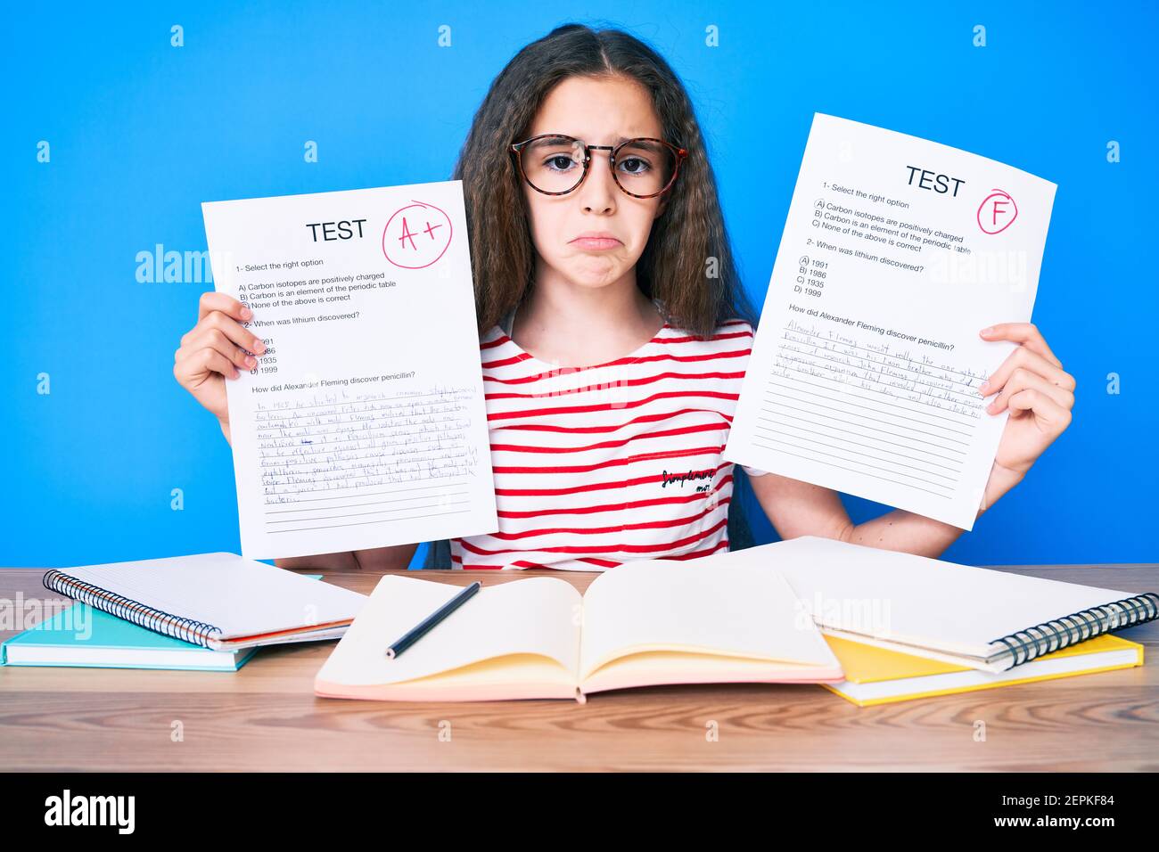 Cute hispanic girl showing failed and passe exam sitting on the table ...