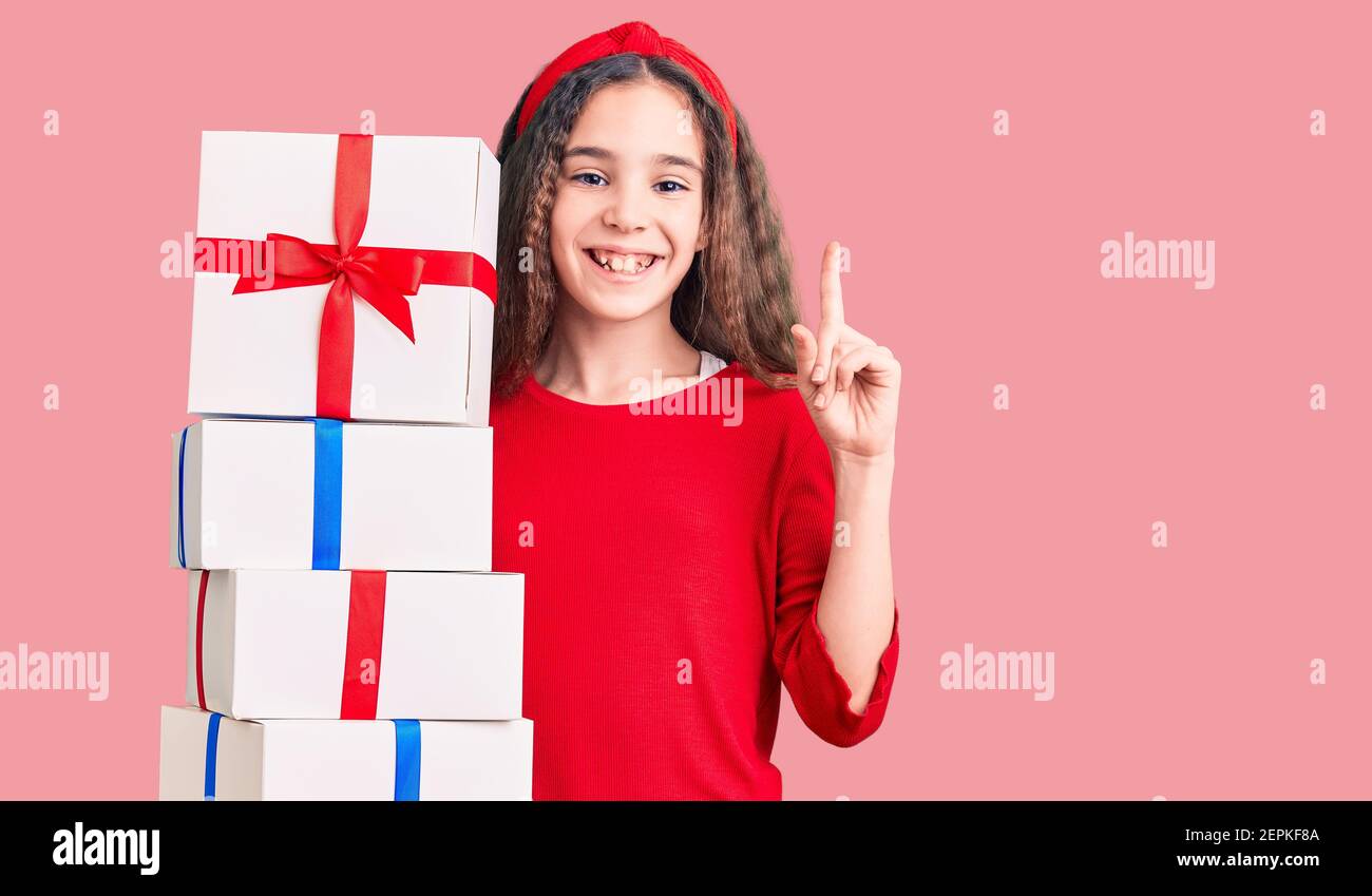 Cute hispanic child girl holding gift surprised with an idea or ...