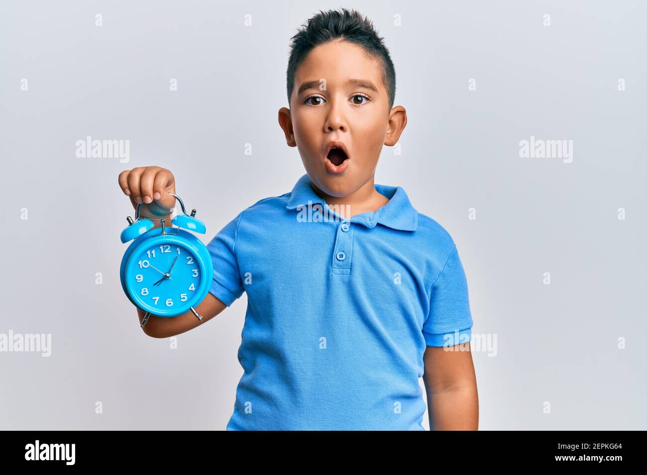 Little boy hispanic kid holding alarm clock scared and amazed with open ...
