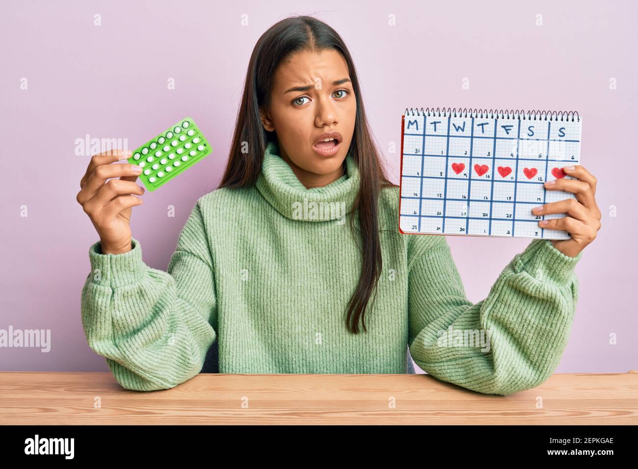 Beautiful hispanic woman holding birth control pills in shock face ...
