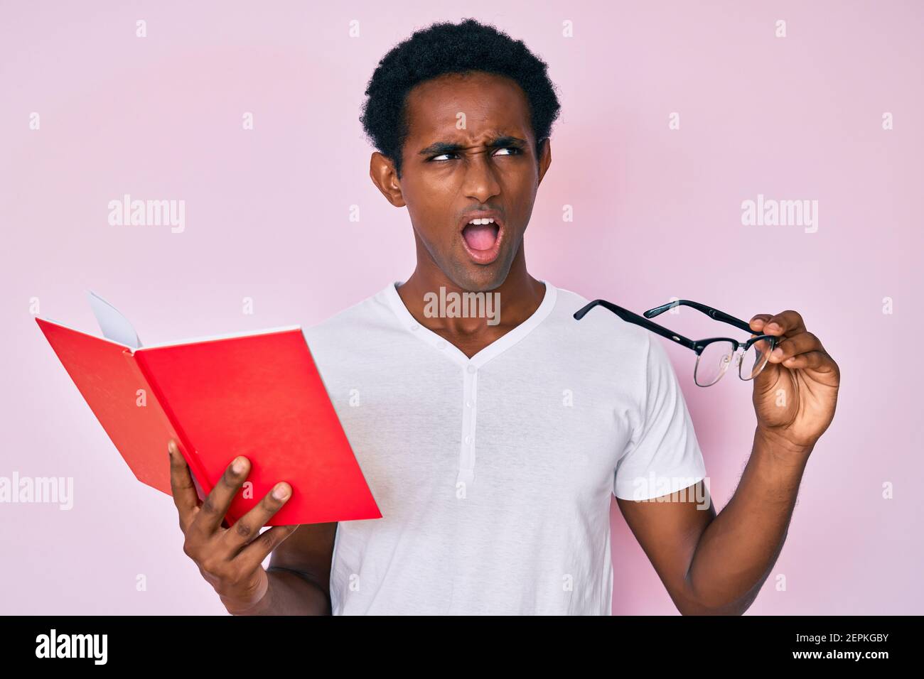 Handsome african man reading a book and holding glasses angry and mad ...