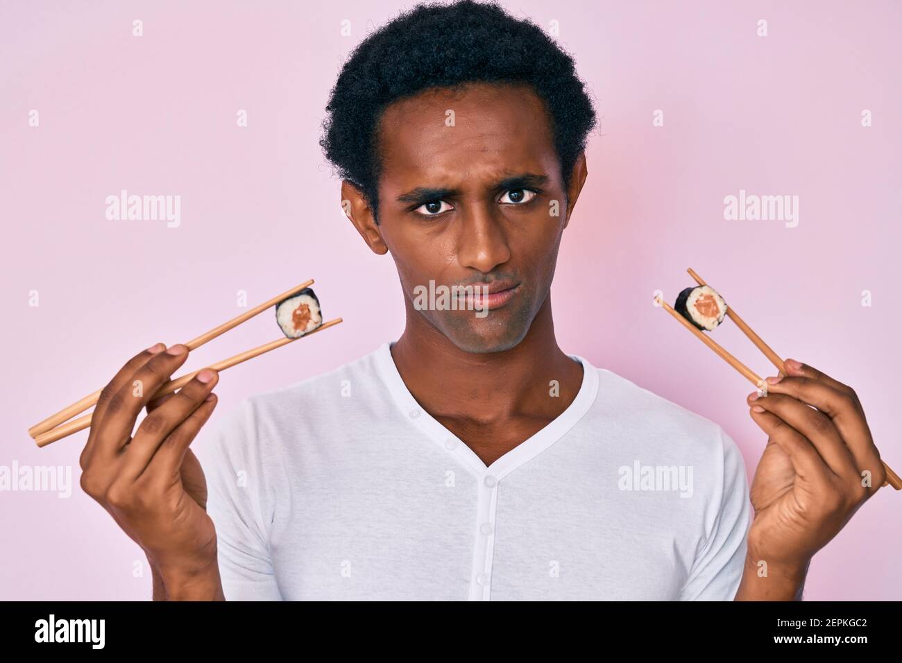 African handsome man eating sushi using chopsticks skeptic and nervous ...