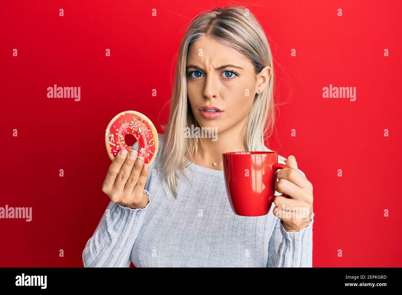 Beautiful blonde woman eating doughnut and drinking coffee clueless and ...