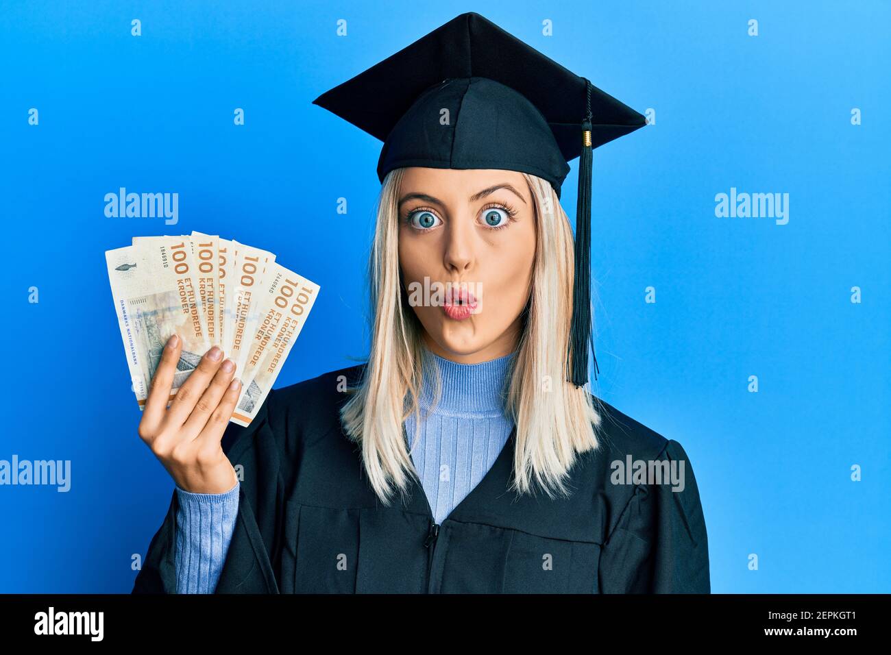 Beautiful blonde woman wearing graduation cap and ceremony robe holding ...
