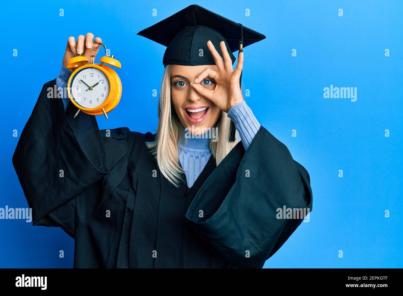 Beautiful blonde woman wearing graduation cap and ceremony robe holding ...