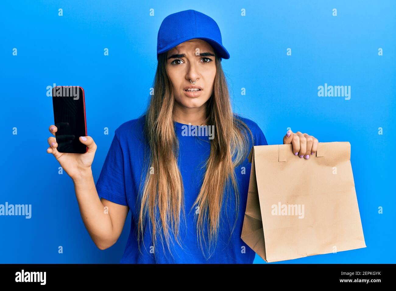 Young hispanic woman holding delivery paper bag and showing smartphone ...
