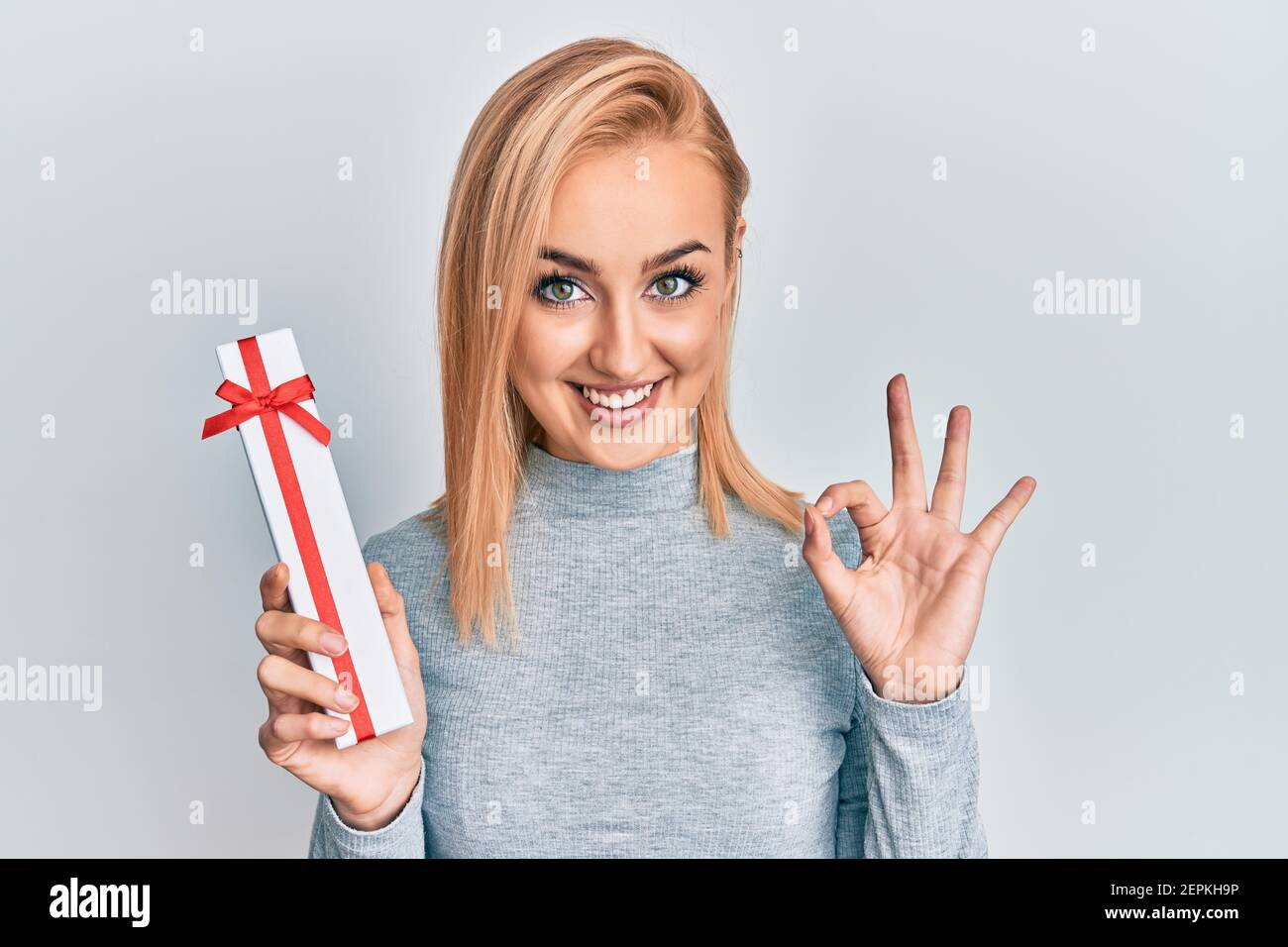 Beautiful caucasian woman holding gift doing ok sign with fingers ...