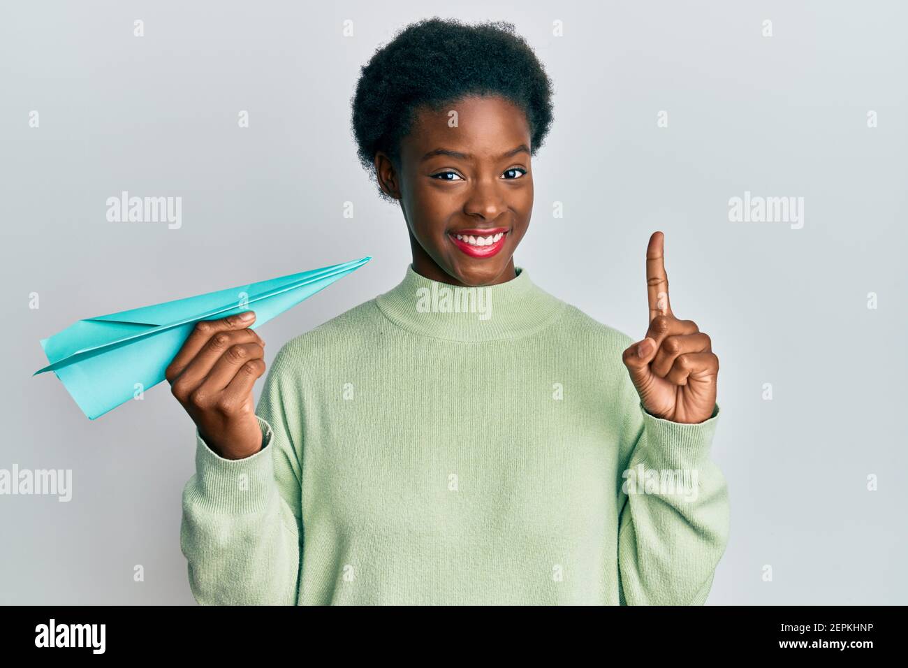 Young african american girl holding paper airplane smiling with an idea ...