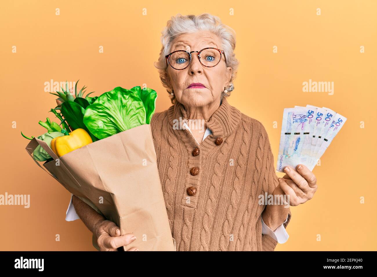 Senior grey-haired woman holding groceries and colombian pesos ...