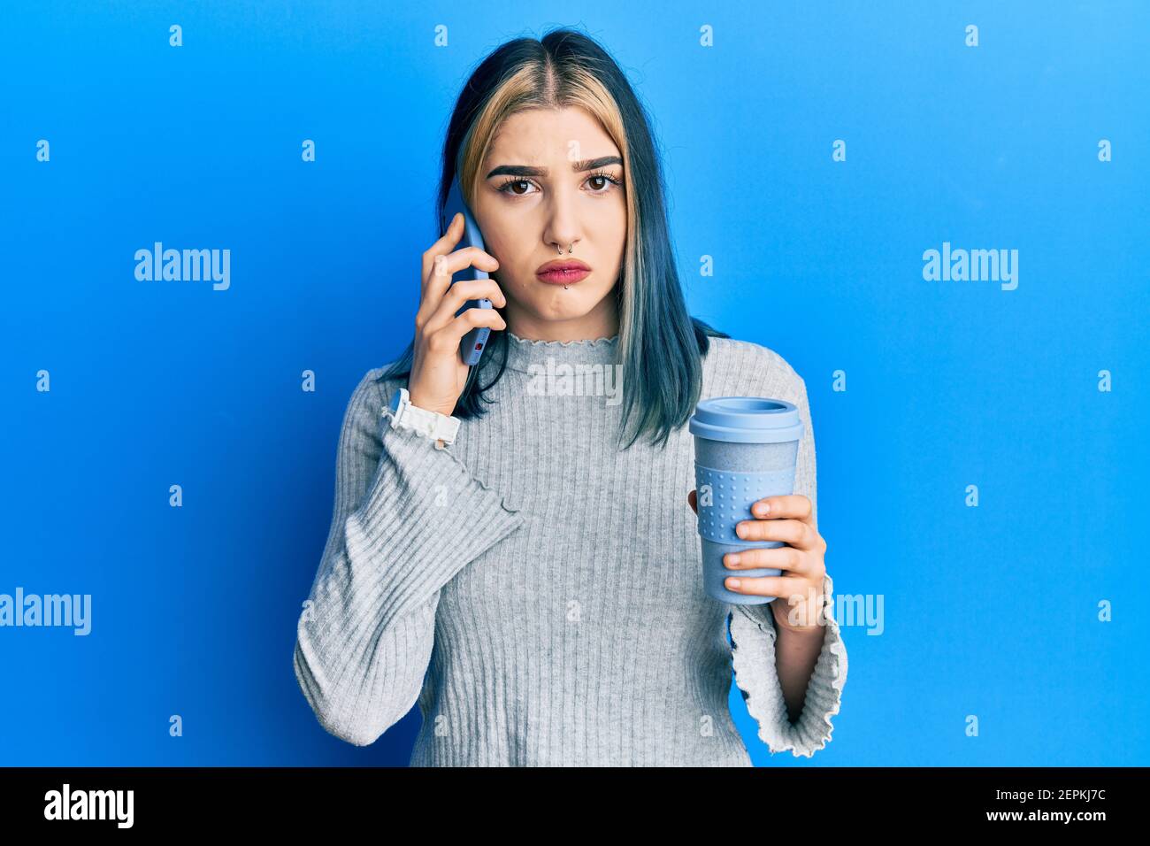 Young modern girl using smartphone and drinking a cup of coffee ...
