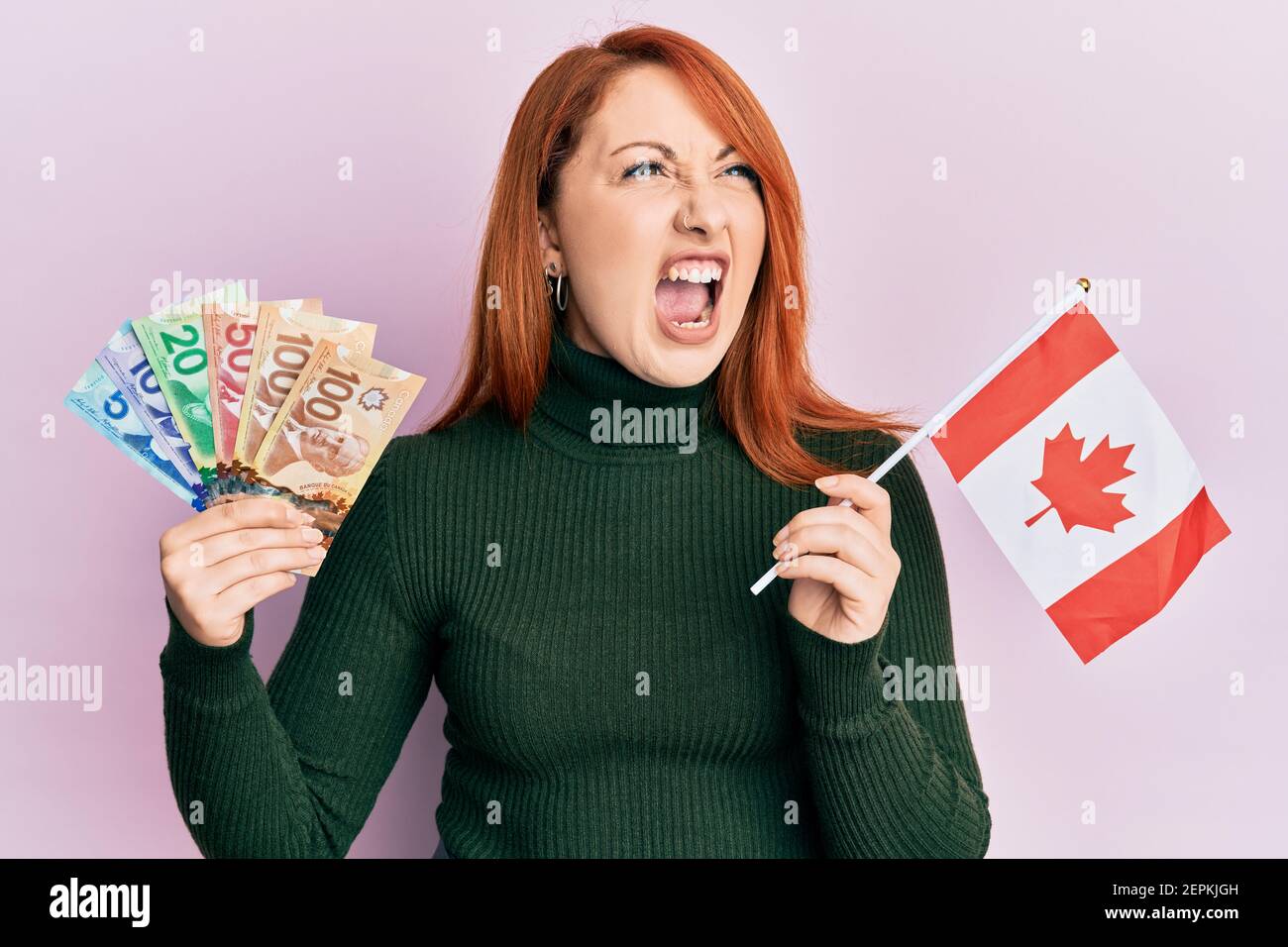 Beautiful redhead woman holding canadian dollars and canada flag angry ...