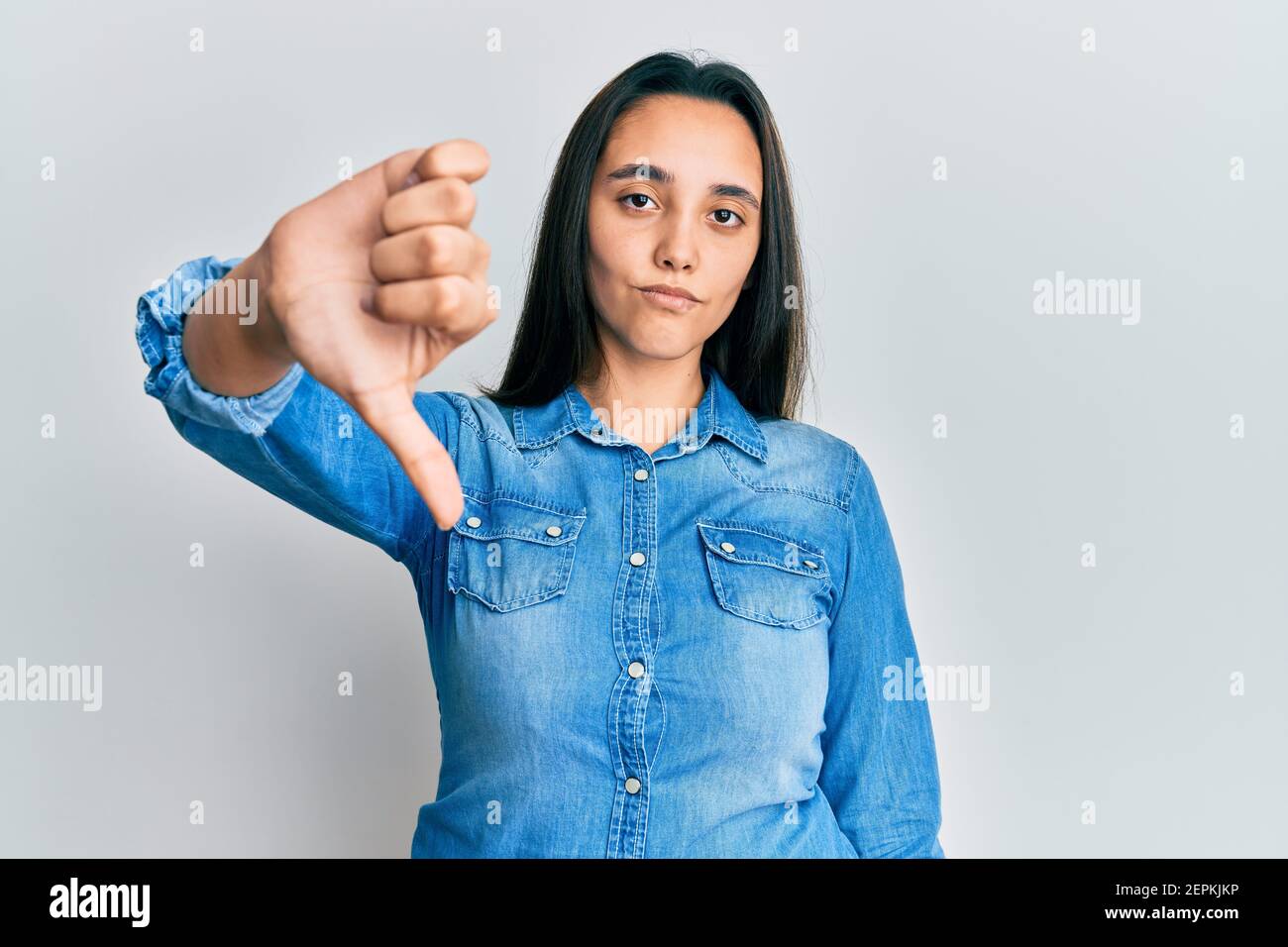 Young hispanic woman wearing casual denim jacket looking unhappy and ...