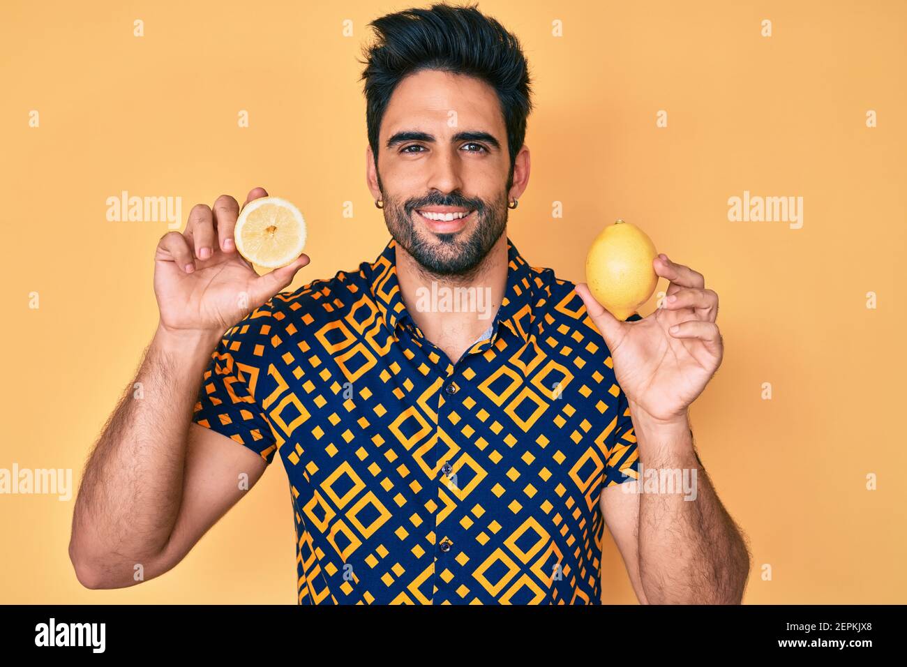 Handsome hispanic man with beard holding lemon smiling with a happy and ...