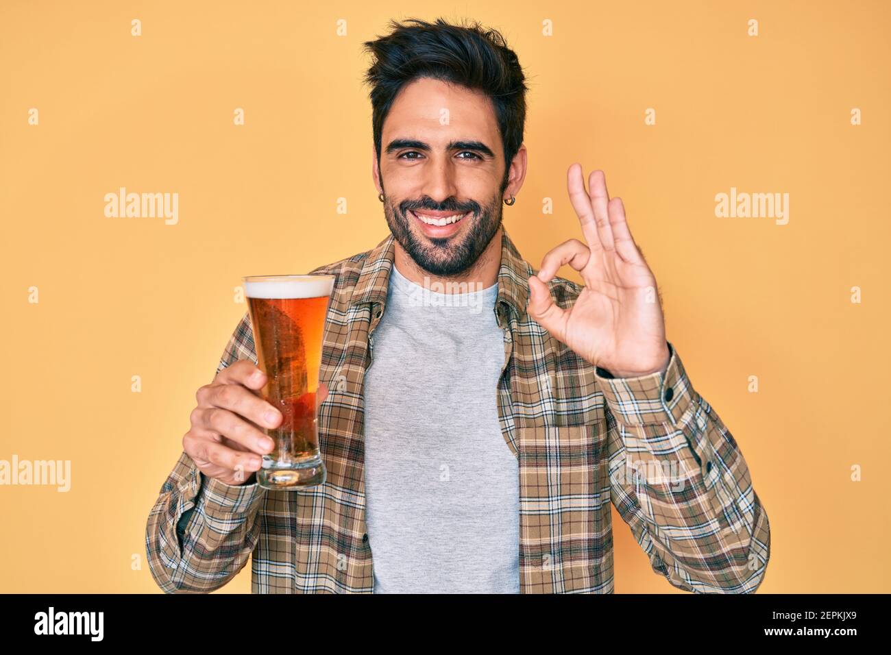 Handsome hispanic man with beard drinking a pint of beer doing ok sign ...
