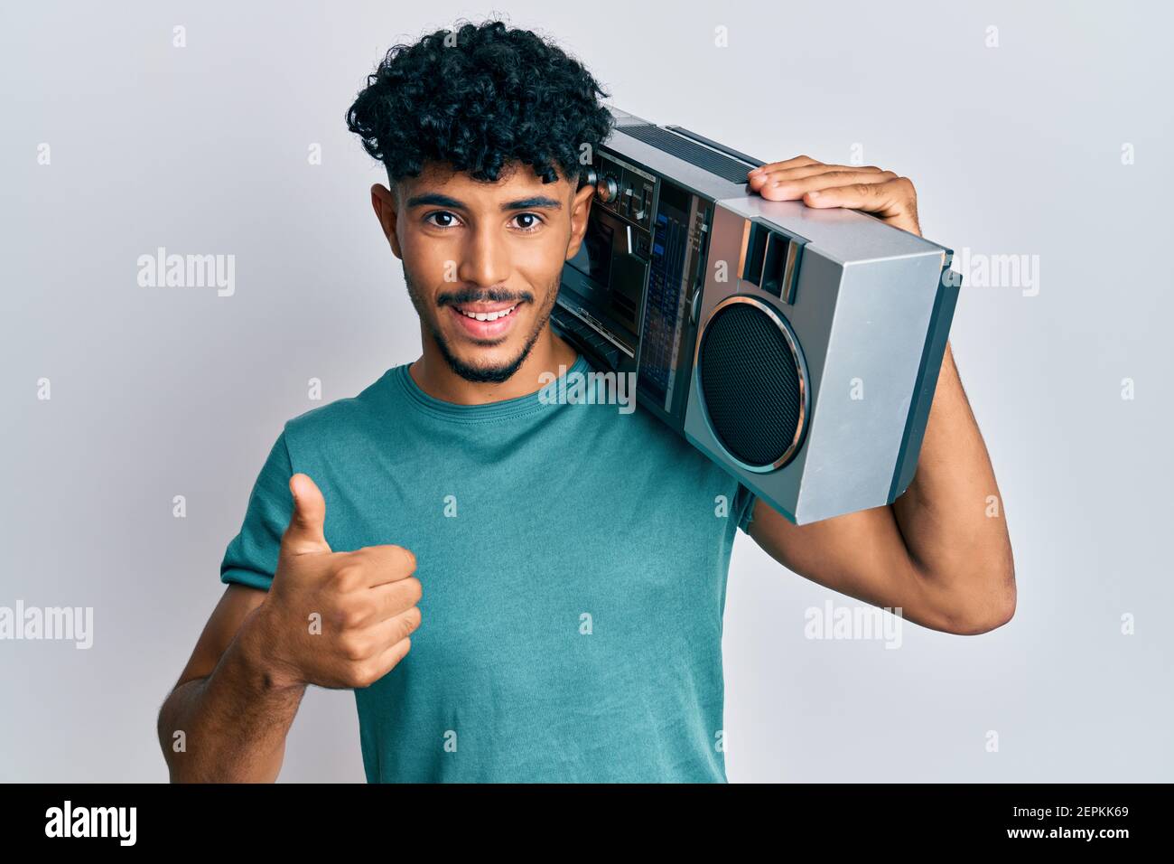 Young arab handsome man holding boombox, listening to music smiling ...