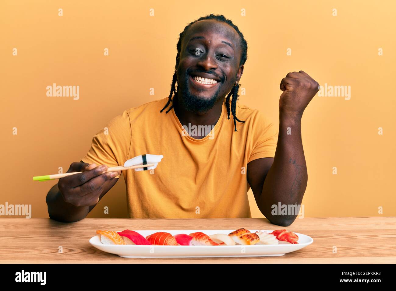 Handsome young black man eating sushi sitting on the table screaming ...