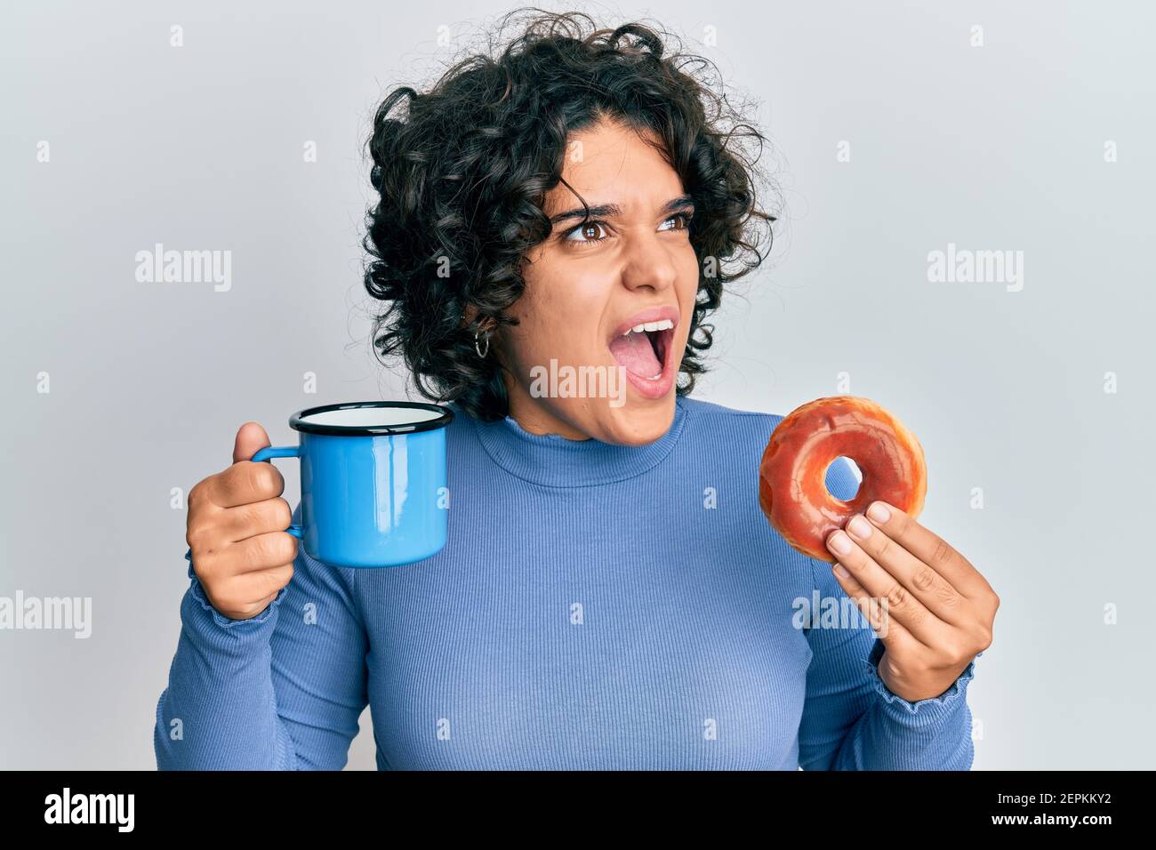Young hispanic woman with curly hair drinking a cup of coffee and ...