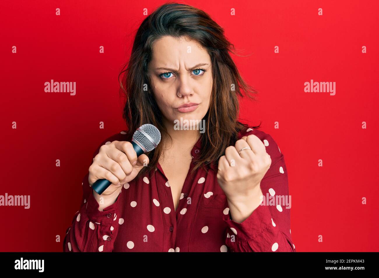 Young caucasian woman singing song using microphone annoyed and ...
