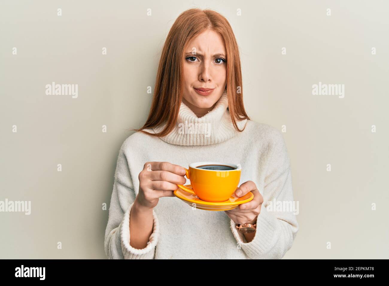 Young irish woman drinking a cup of coffee skeptic and nervous ...