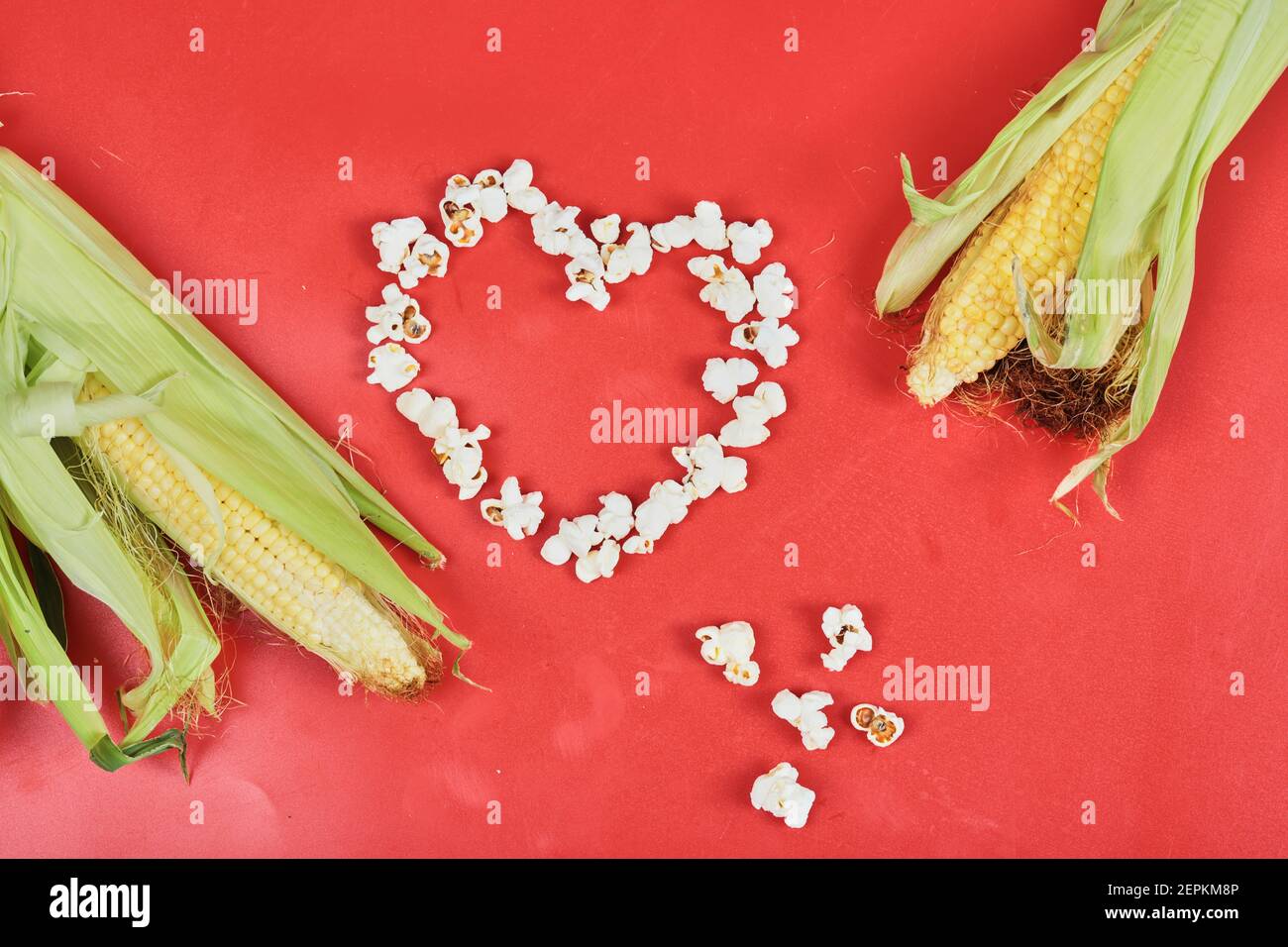 Two corns and popcorn shaped like heart on red background Stock Photo ...
