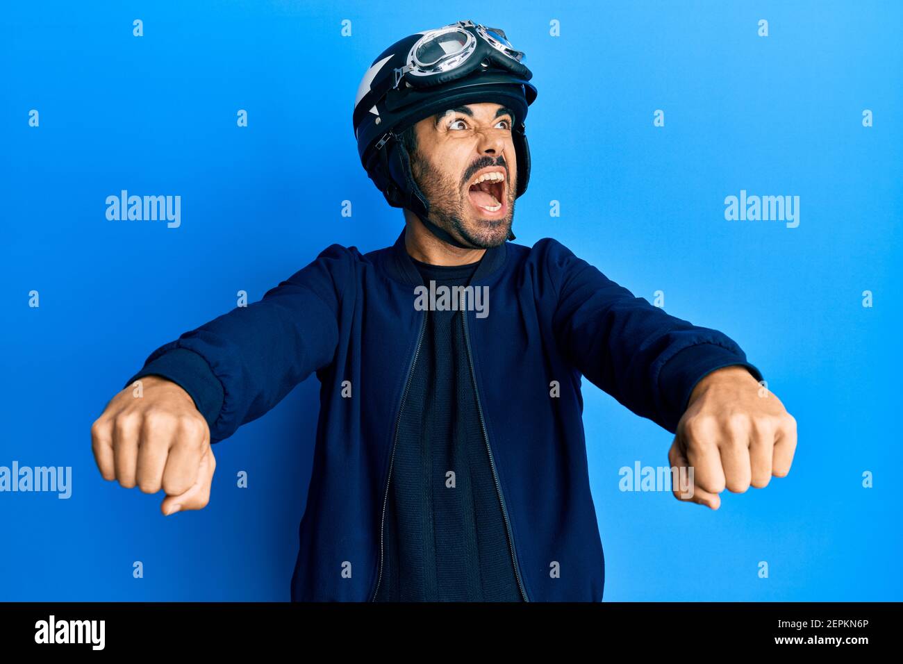 Young hispanic man holding motorcycle helmet angry and mad screaming ...
