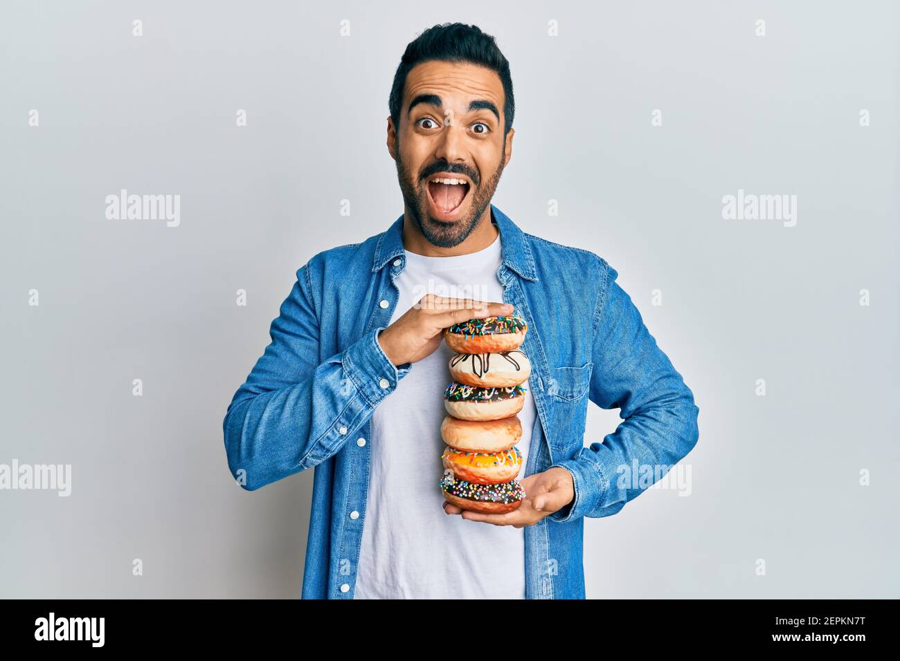 Young hispanic man holding tasty colorful doughnuts celebrating crazy ...