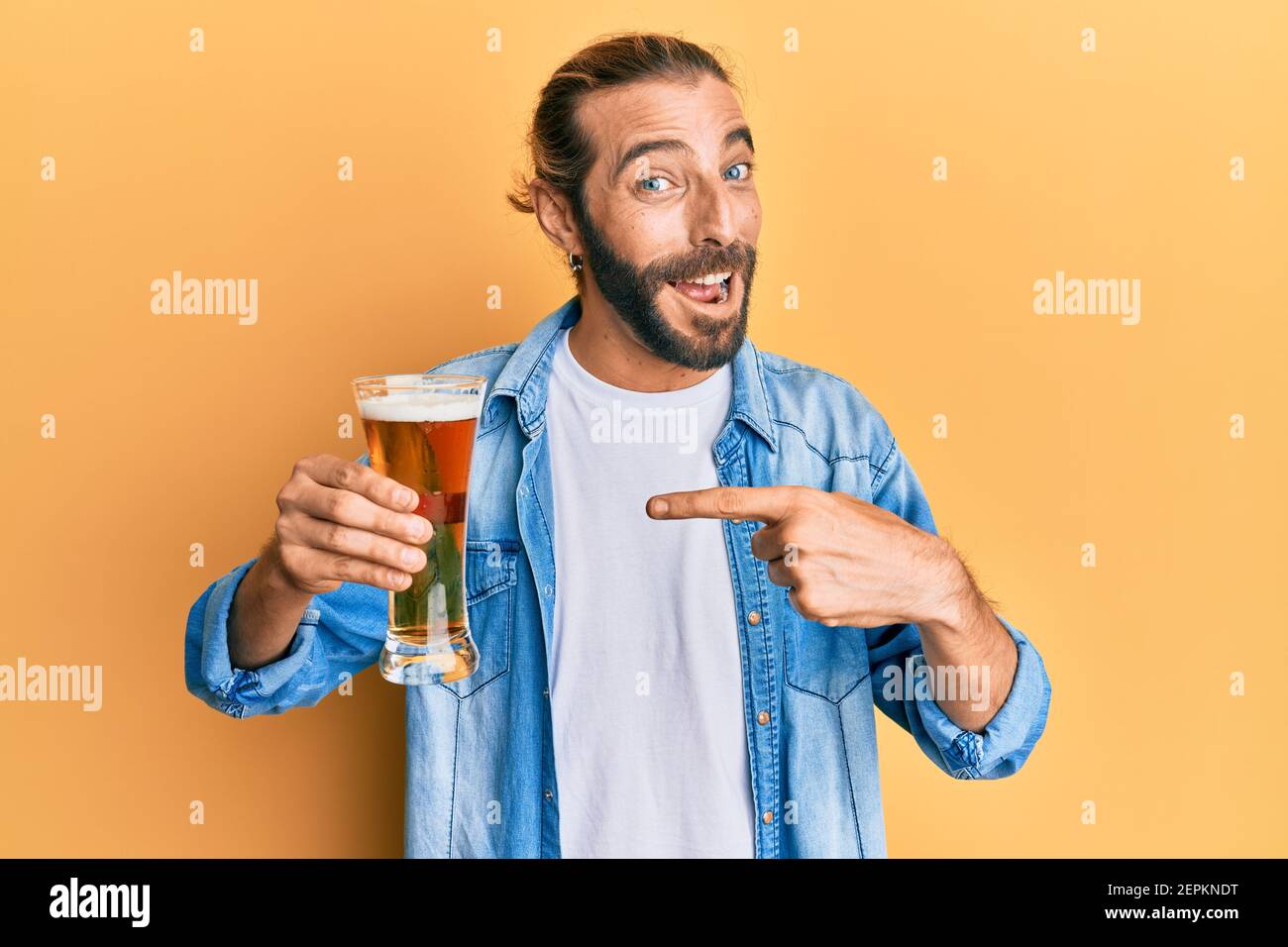 Attractive man with long hair and beard drinking a pint of beer smiling ...