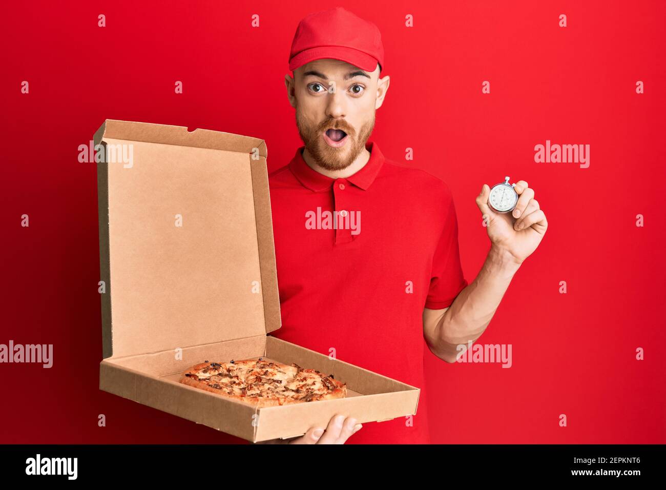 Young redhead man wearing delivery uniform holding pizza box and ...
