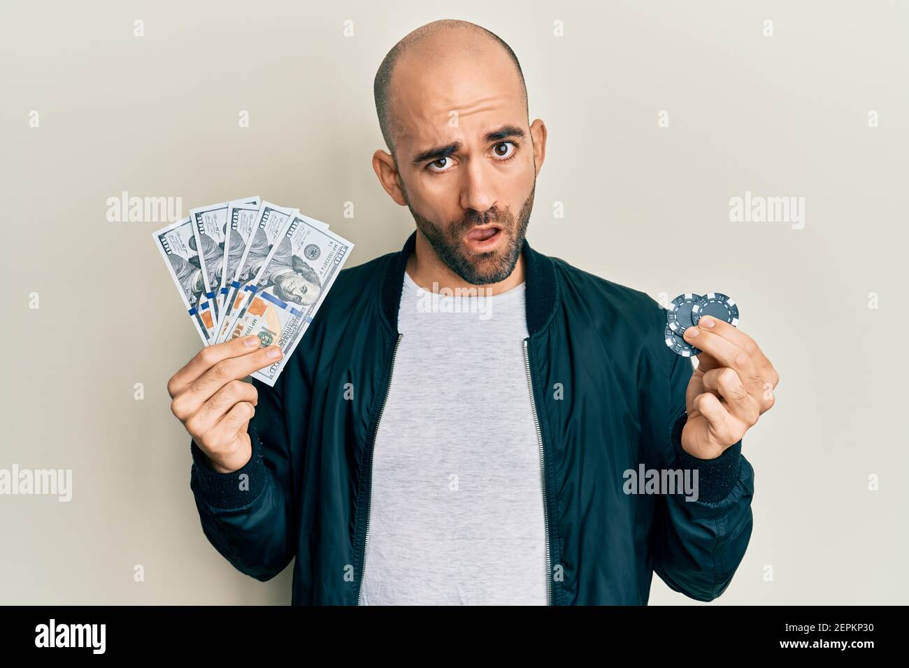 Young hispanic man playing poker holding dollars banknotes and chips in ...