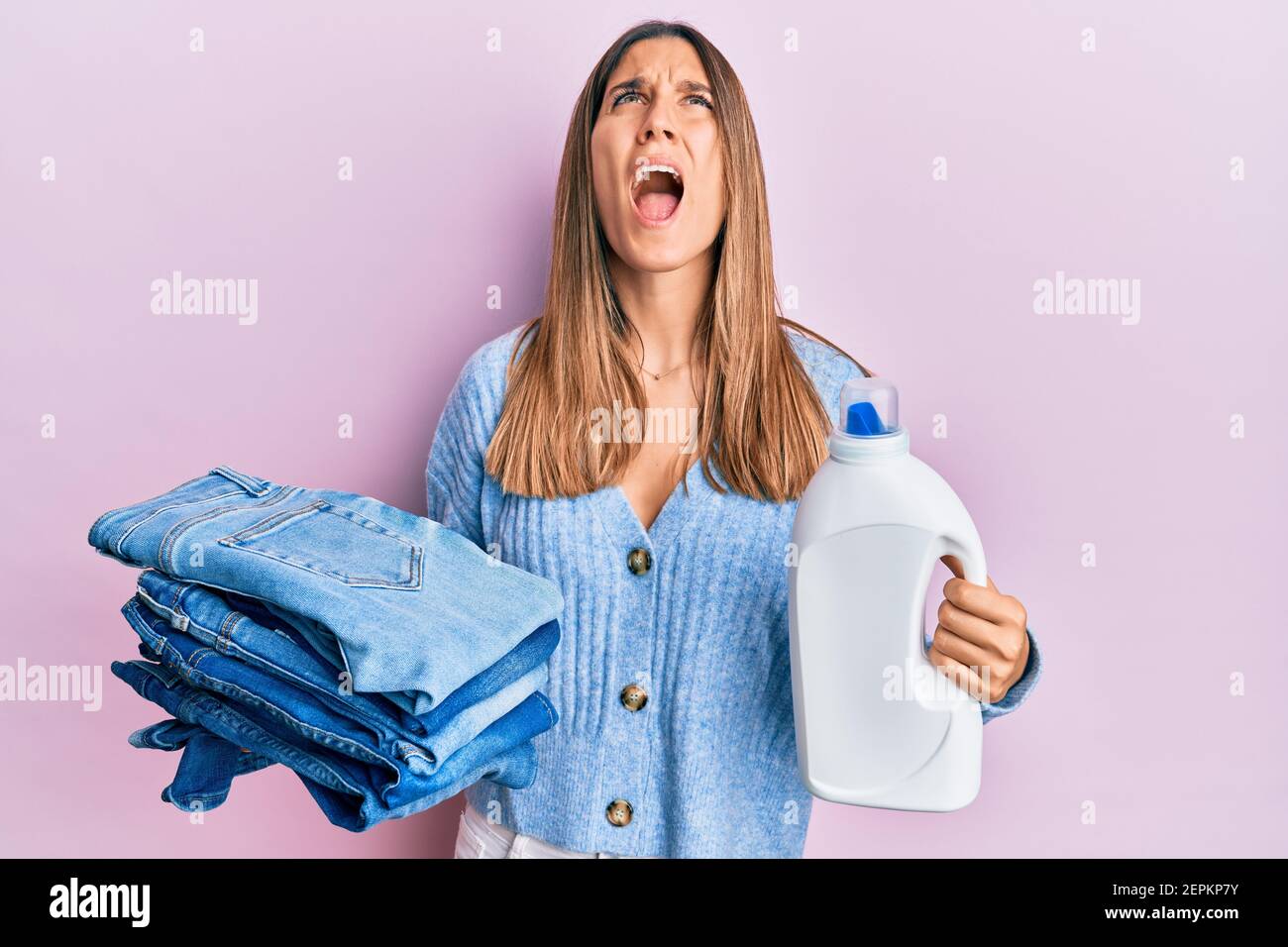 Brunette young woman holding jeans for laundry and detergent bottle ...