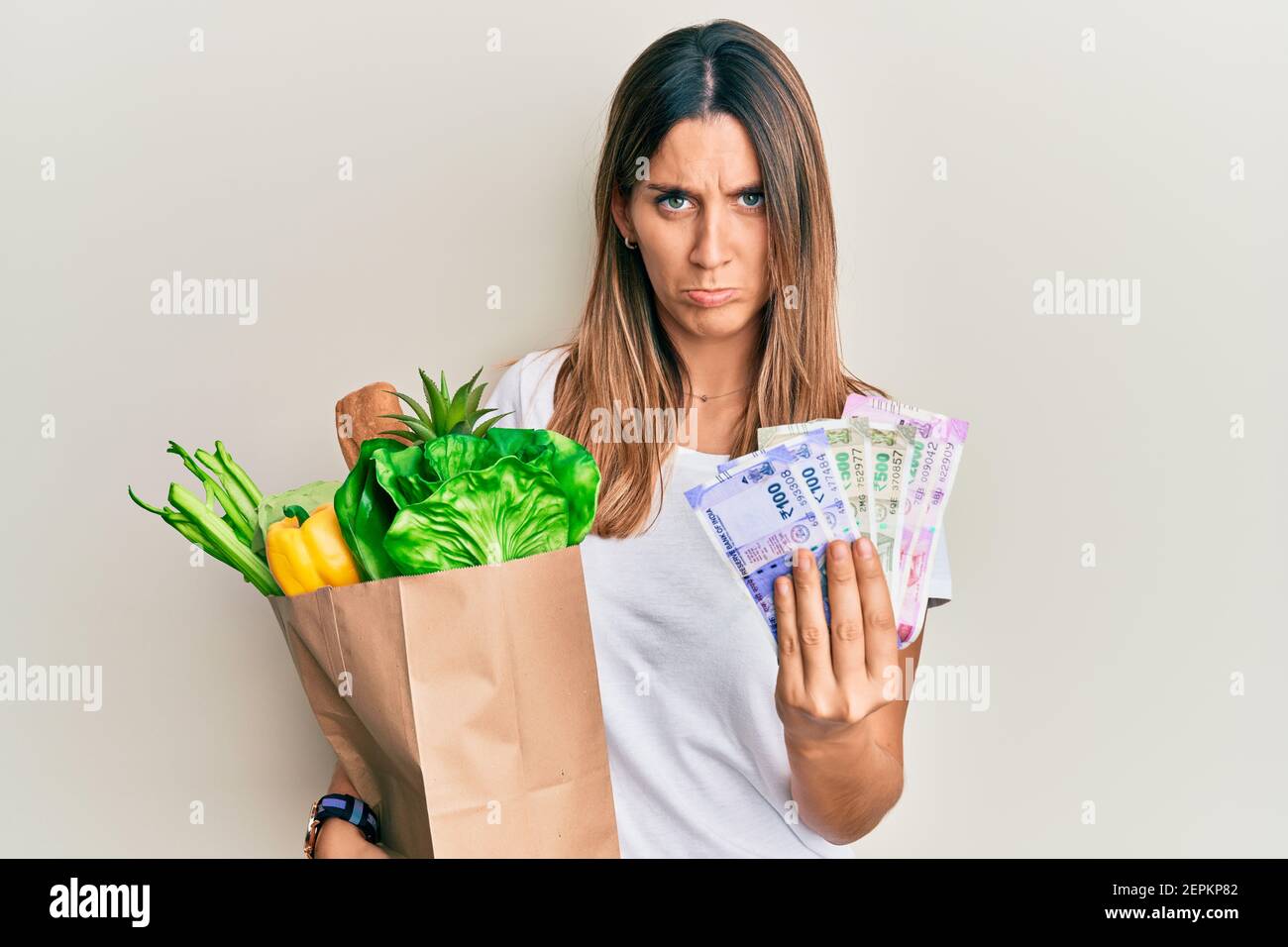 Brunette young woman holding groceries and indian rupee banknotes ...