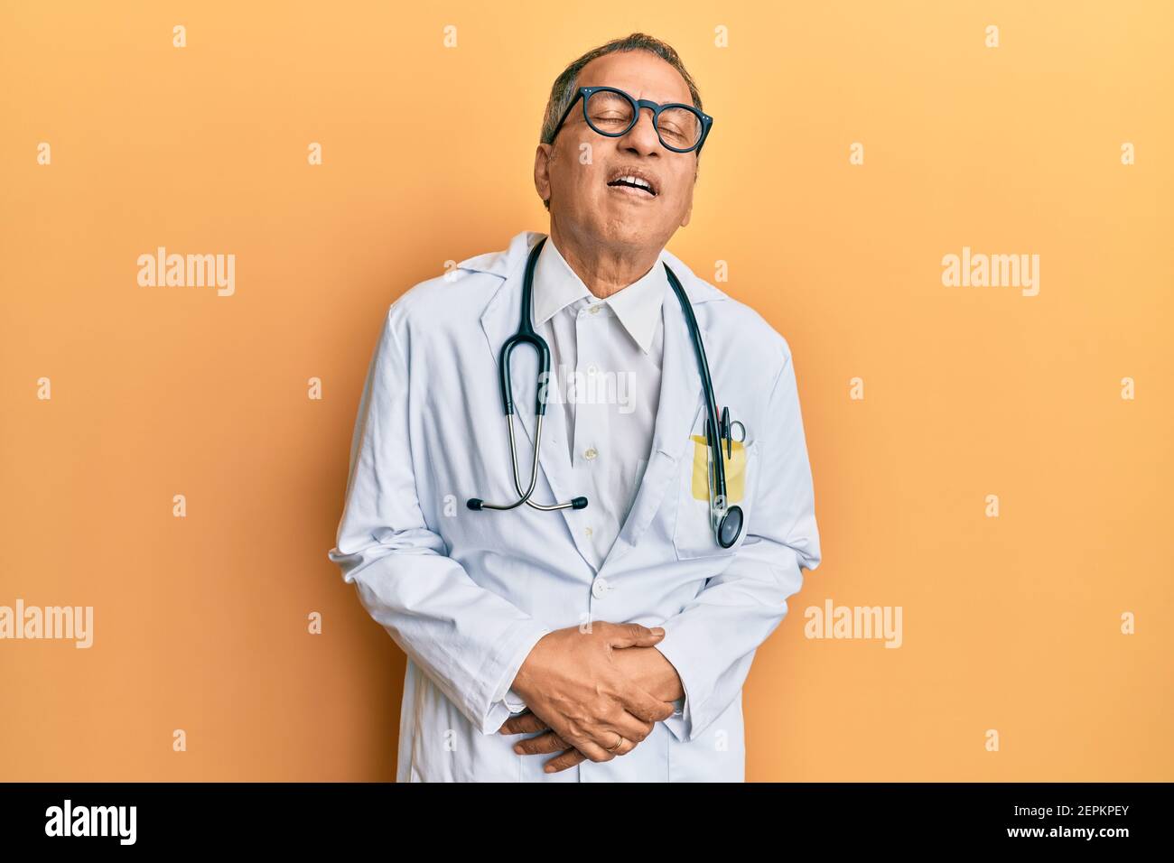 Middle age indian man wearing doctor coat and stethoscope with hand on ...