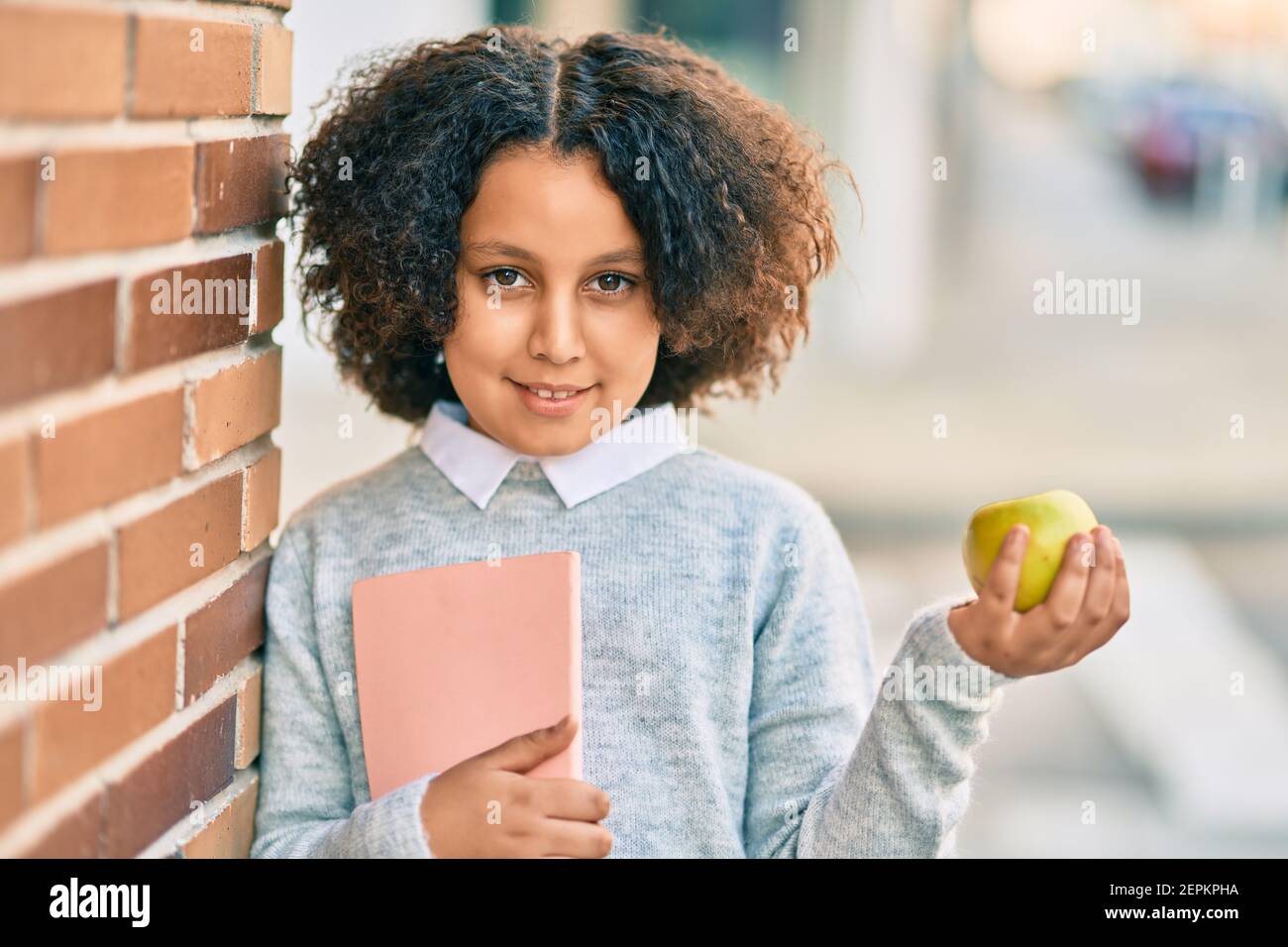 Adorable hispanic student child girl smiling happy holding green apple ...
