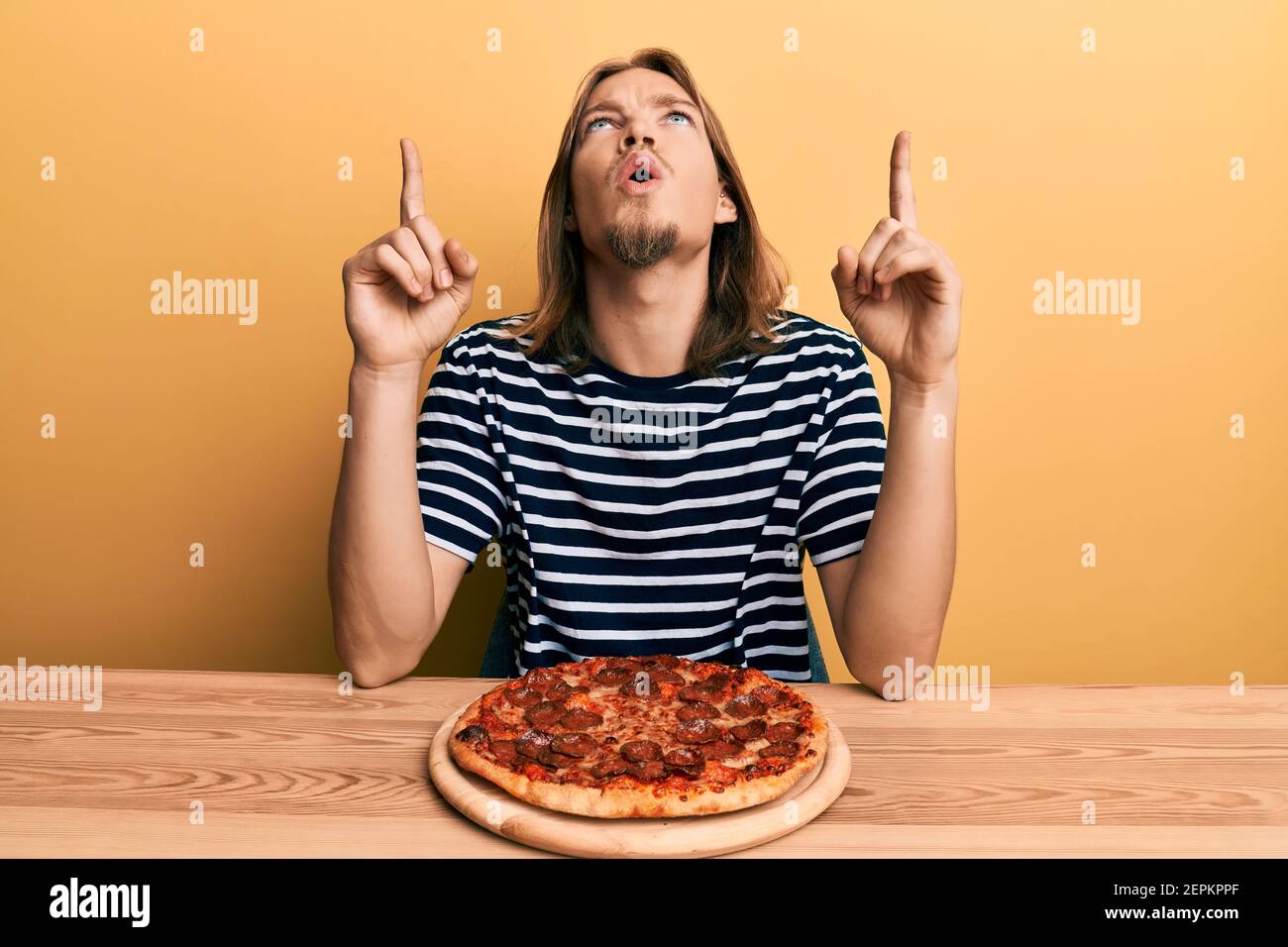 Handsome caucasian man with long hair eating tasty pepperoni pizza ...