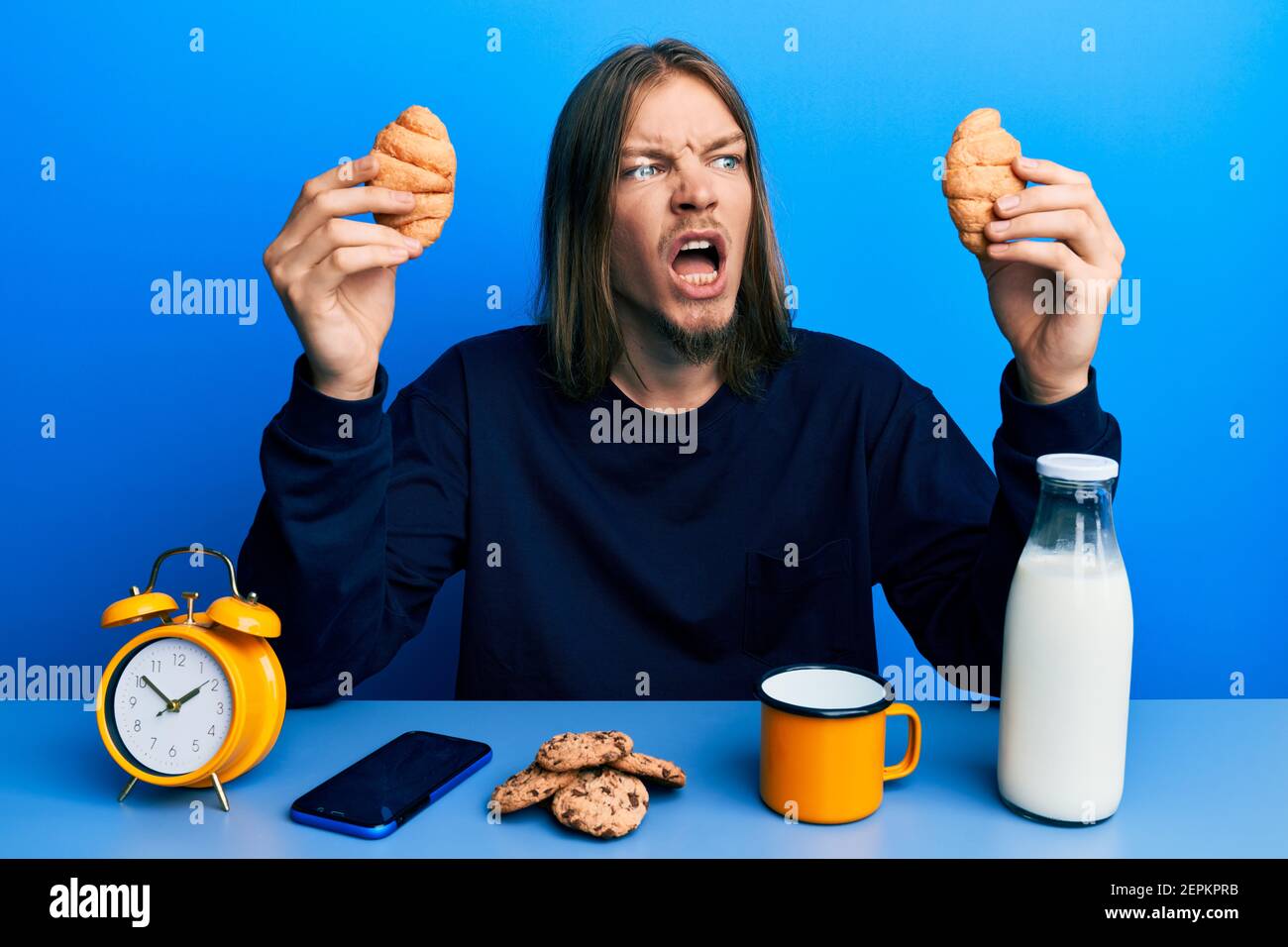 Handsome caucasian man with long hair eating croissant for breakfast ...