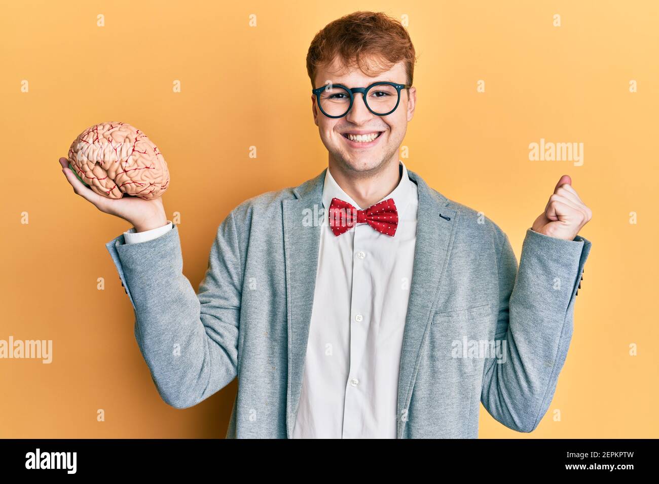 Young caucasian man wearing glasses holding brain screaming proud ...