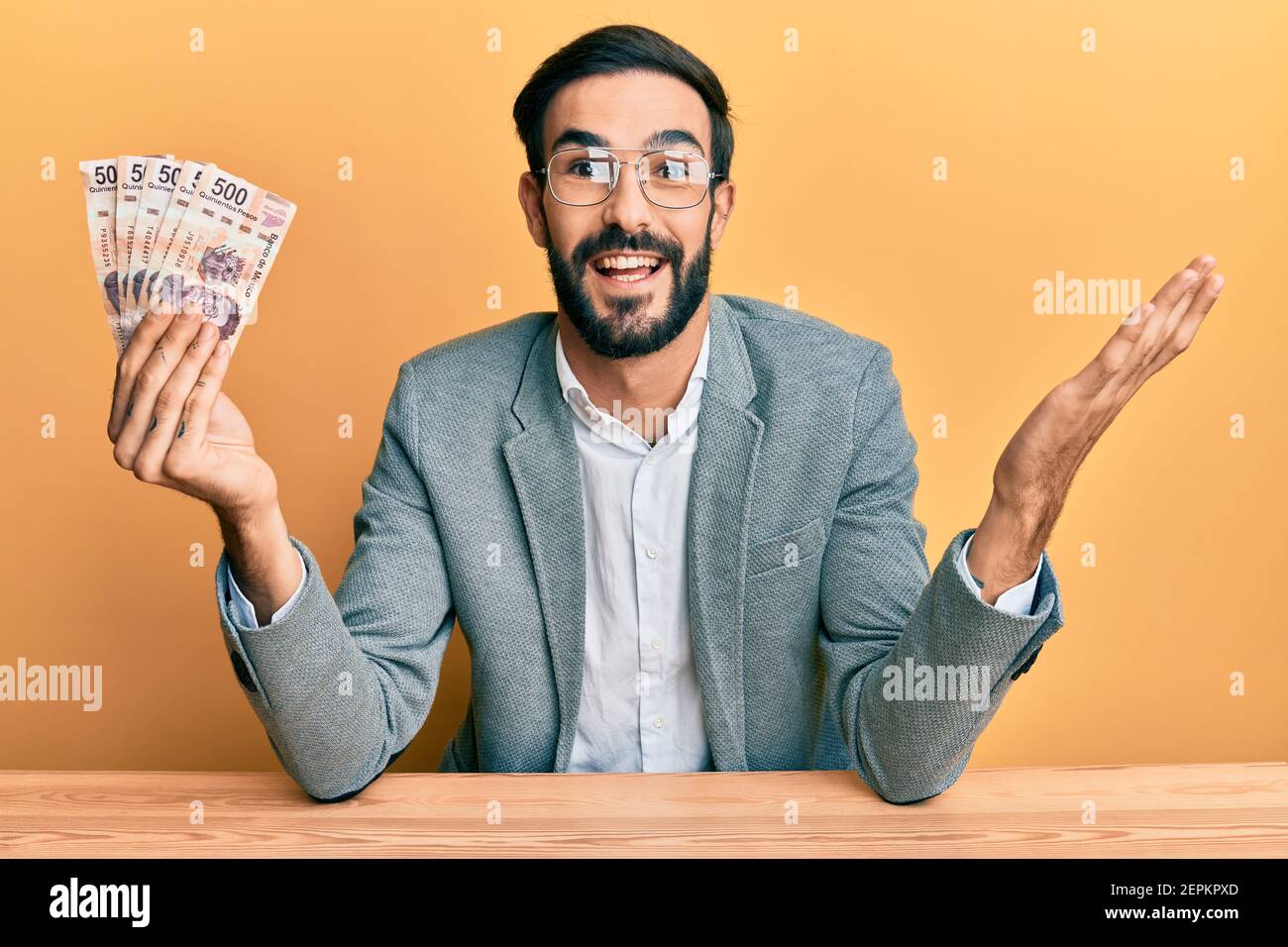 Young hispanic man holding mexican pesos sitting on the table ...