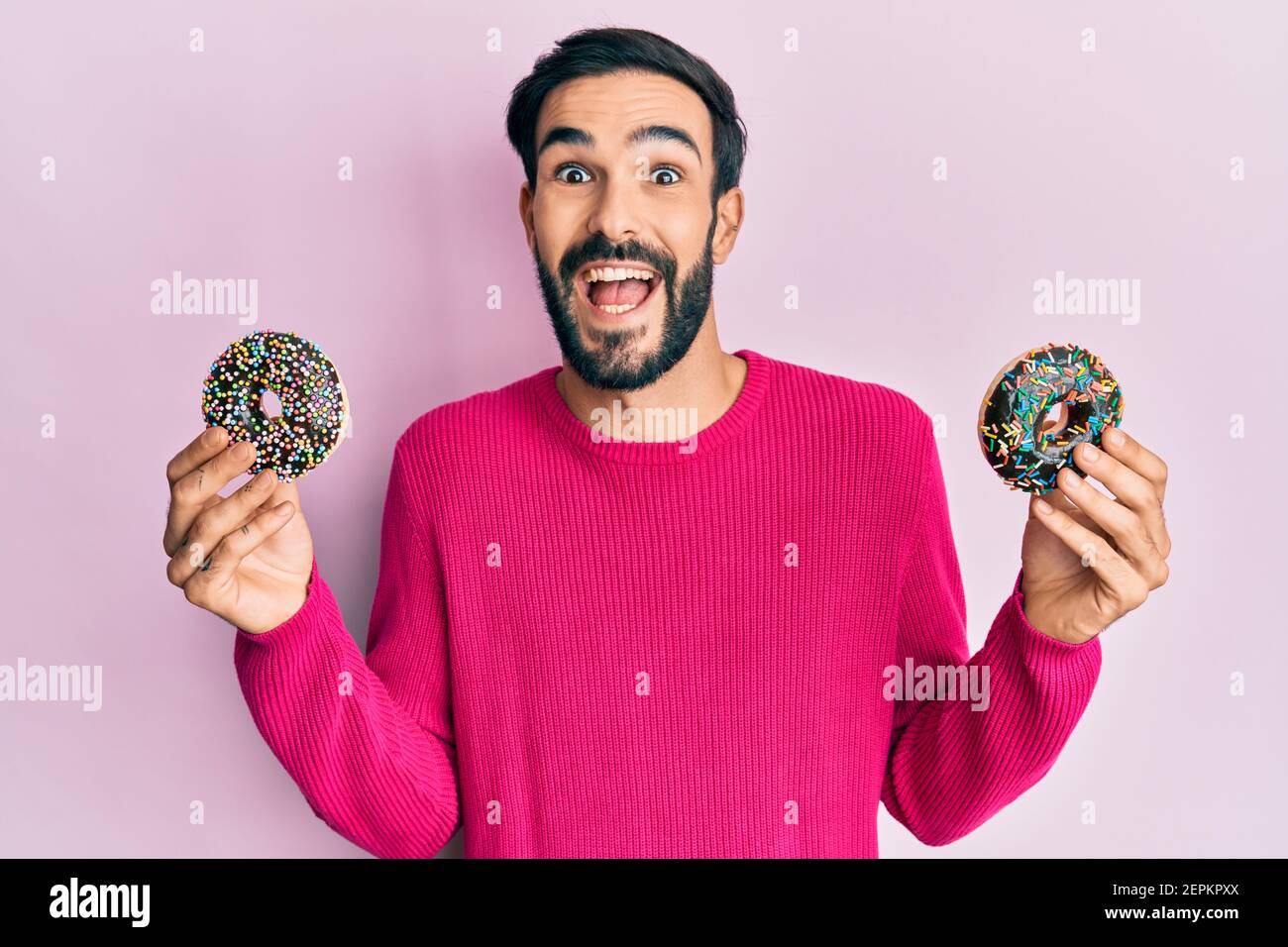 Young hispanic man holding tasty colorful doughnuts celebrating crazy ...