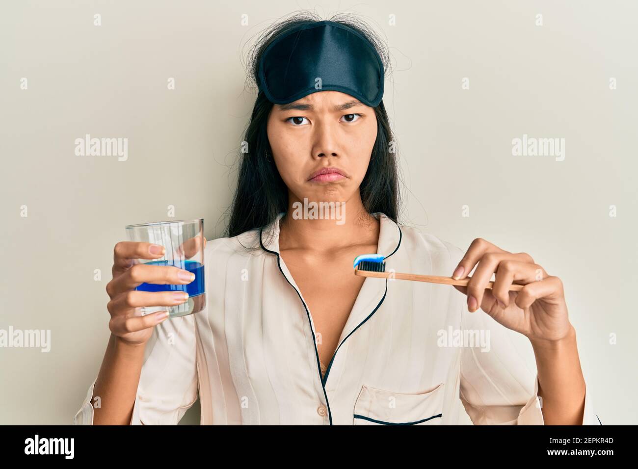 Young chinese woman wearing pajama using toothbrush and mouthwash ...
