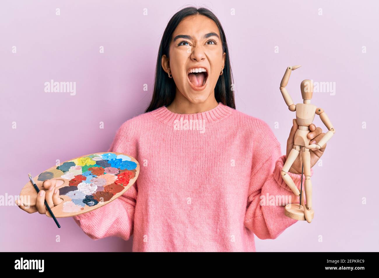 Young asian woman holding painter palette and art manikin angry and mad ...