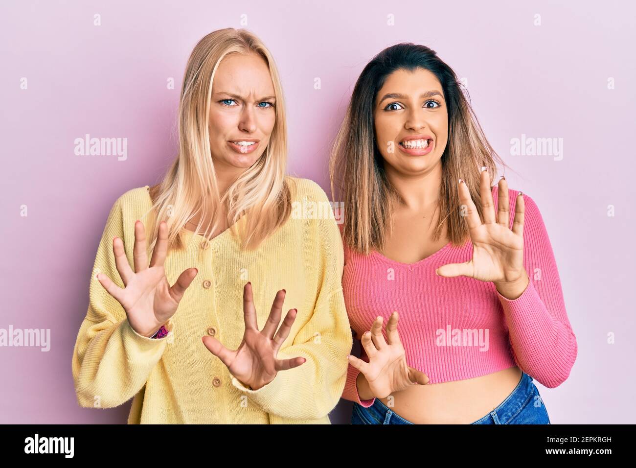 Two friends standing together over pink background disgusted expression ...