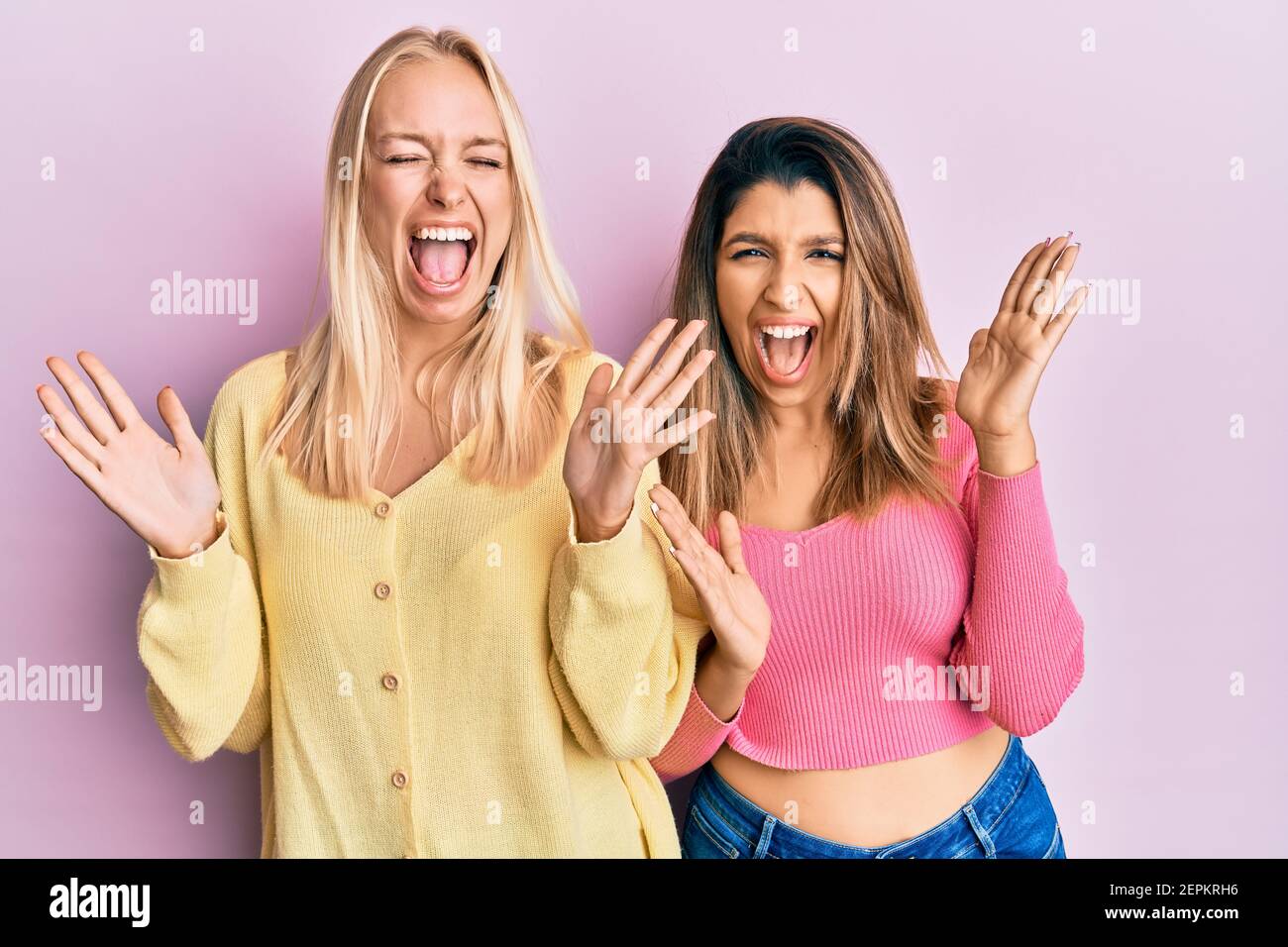 Two friends standing together over pink background celebrating mad and ...