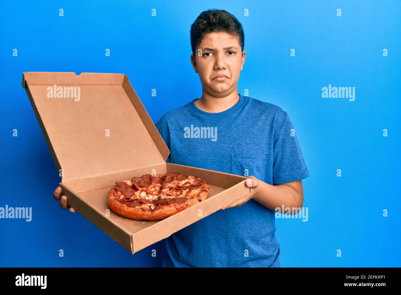 Teenager hispanic boy eating tasty pepperoni pizza depressed and worry ...