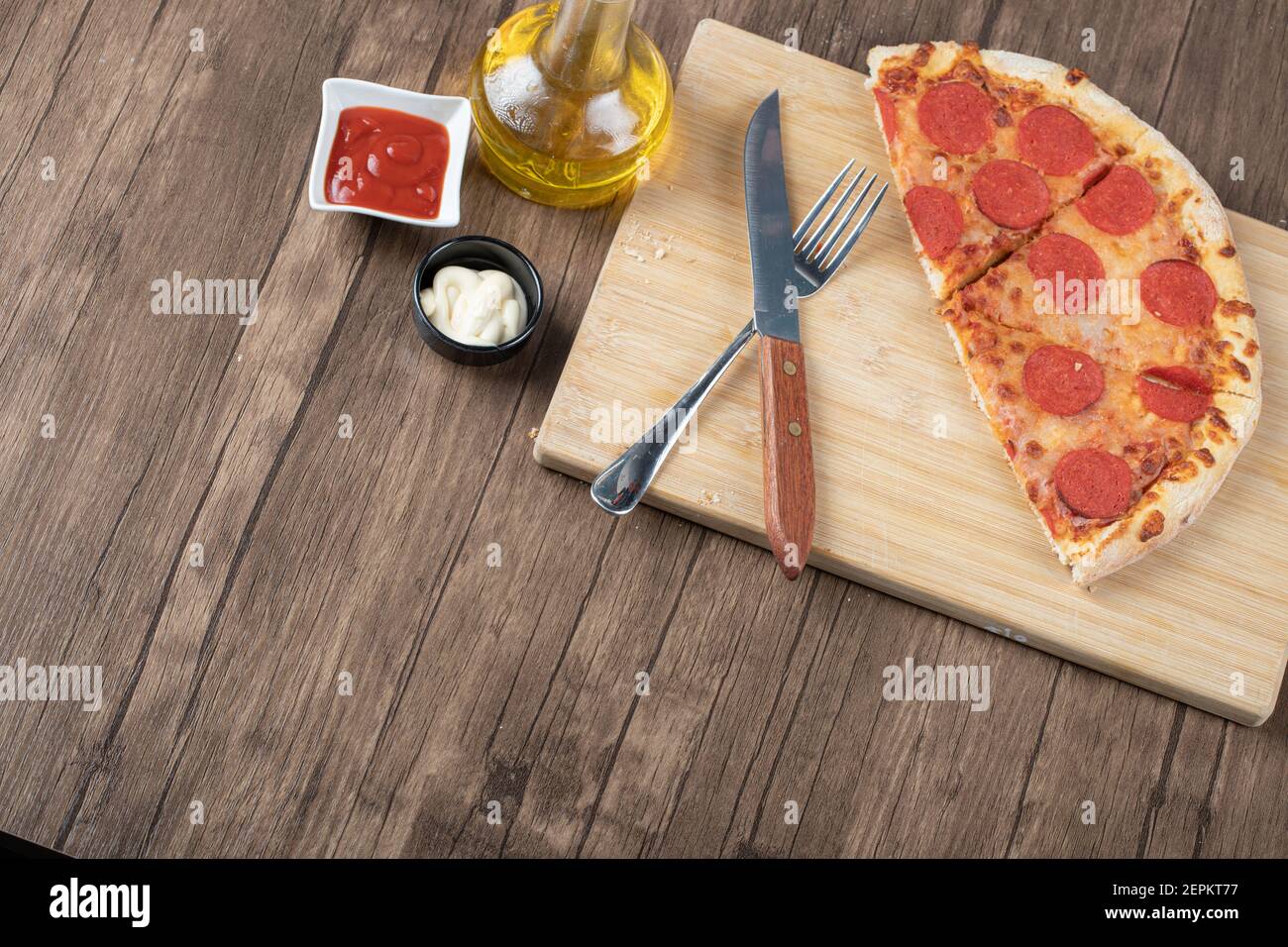 Wide angle photo of Half of pepperoni pizza on wooden plate with sauces and oil Stock Photo - Alamy
