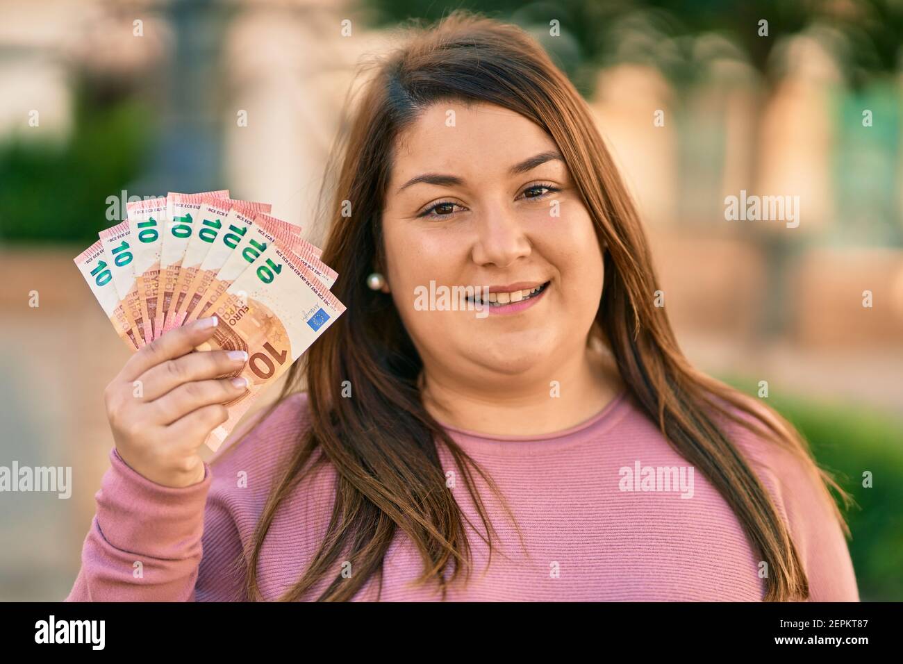 Young hispanic plus size woman smiling happy holding 10 euro banknotes ...