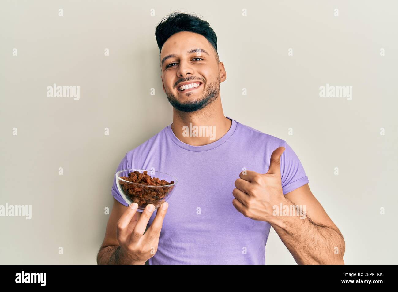 Young arab man holding raisins bowl smiling happy and positive, thumb ...