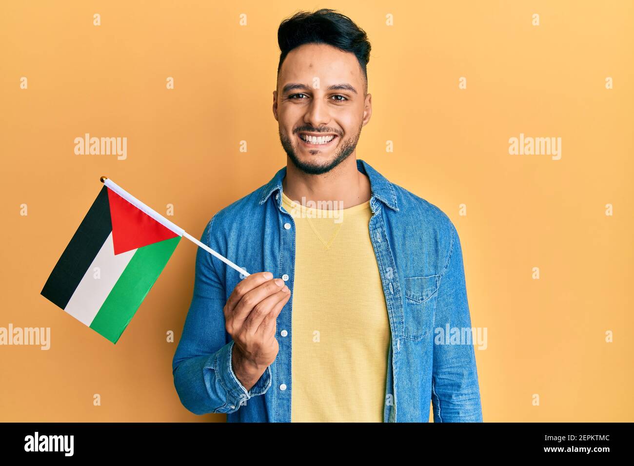 Young arab man holding palestine flag looking positive and happy ...