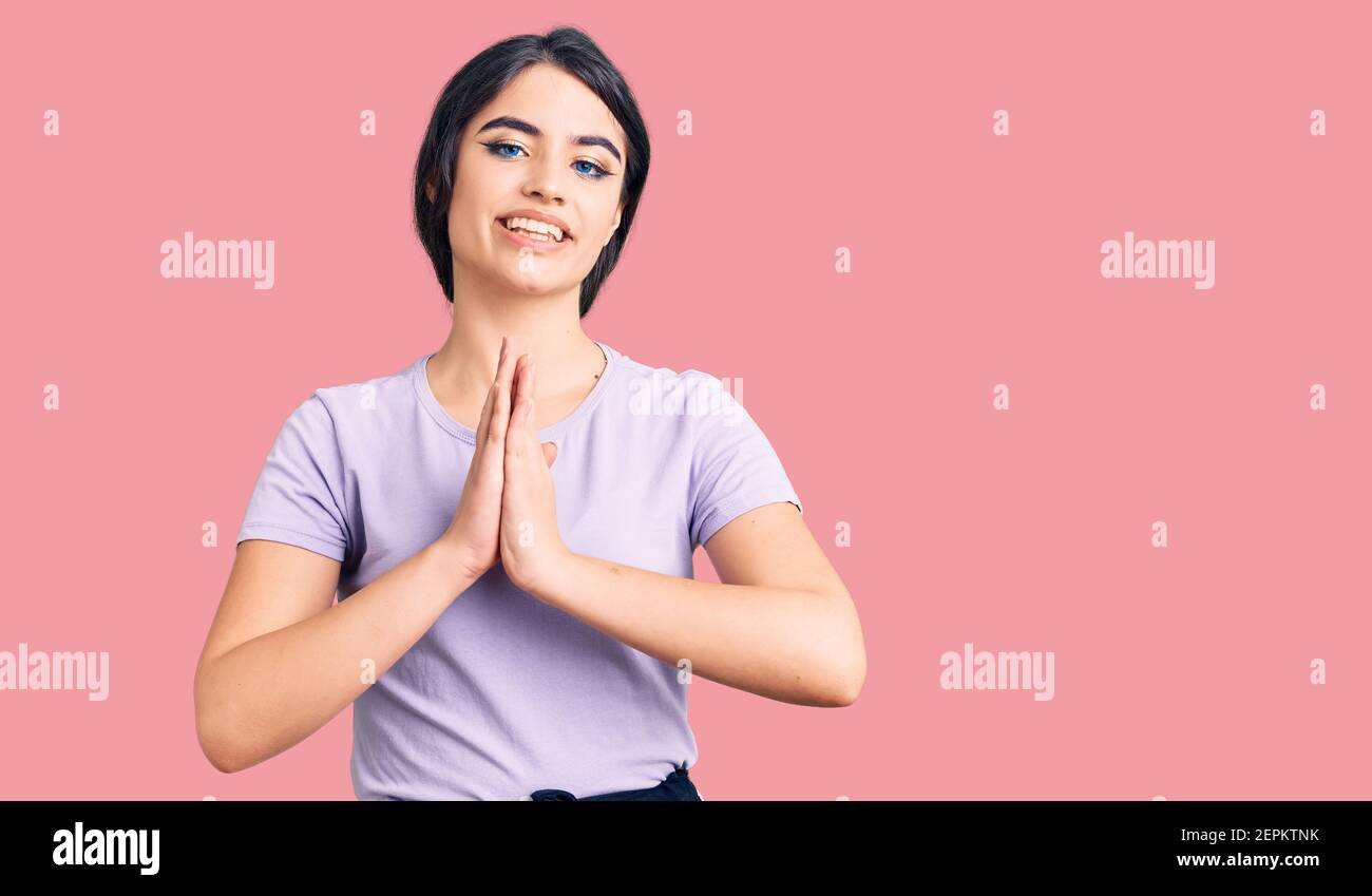 Brunette teenager girl wearing casual clothes praying with hands ...