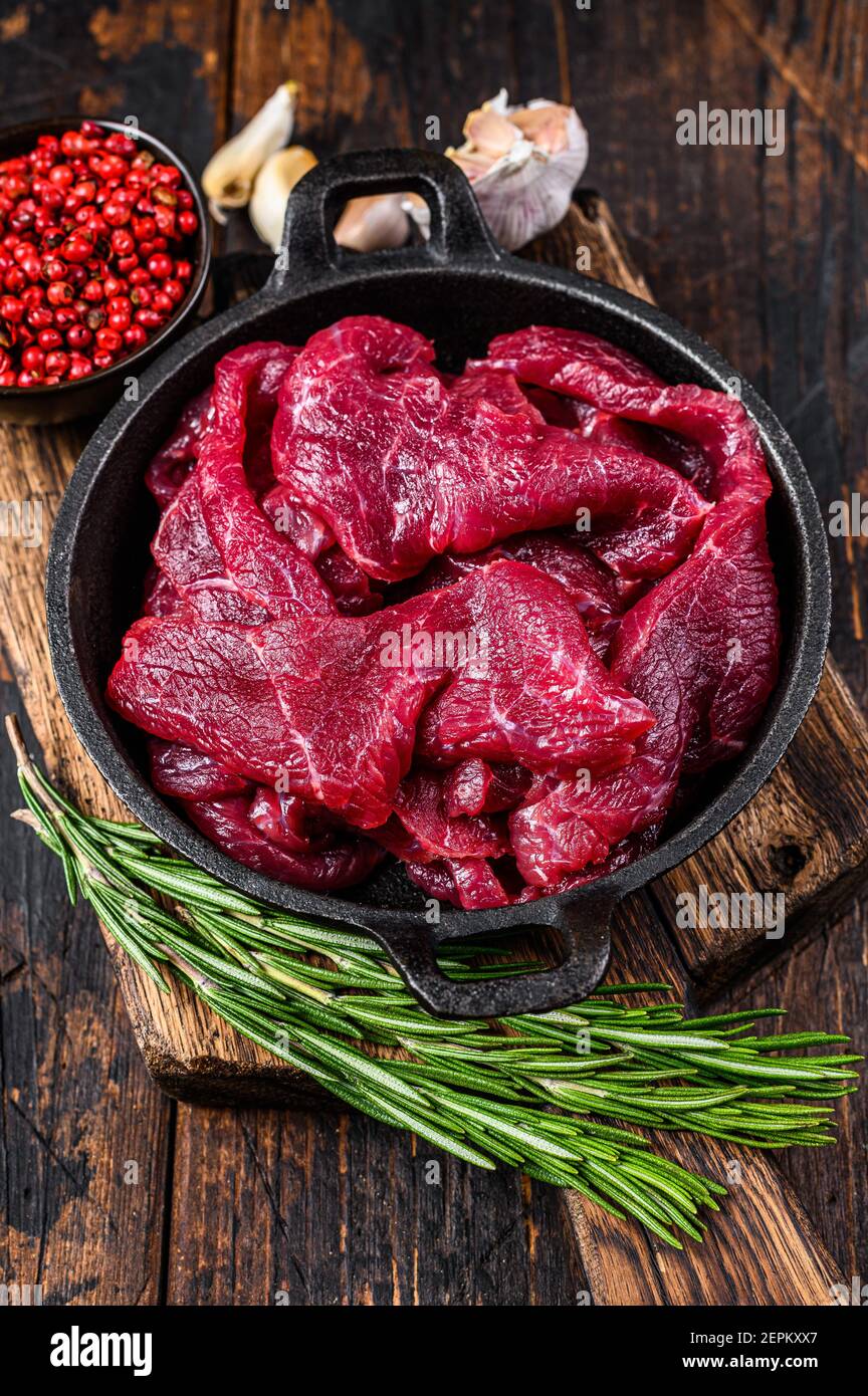 Fresh raw diced slices of red beef fiilet meat in cast iron pan. Dark ...